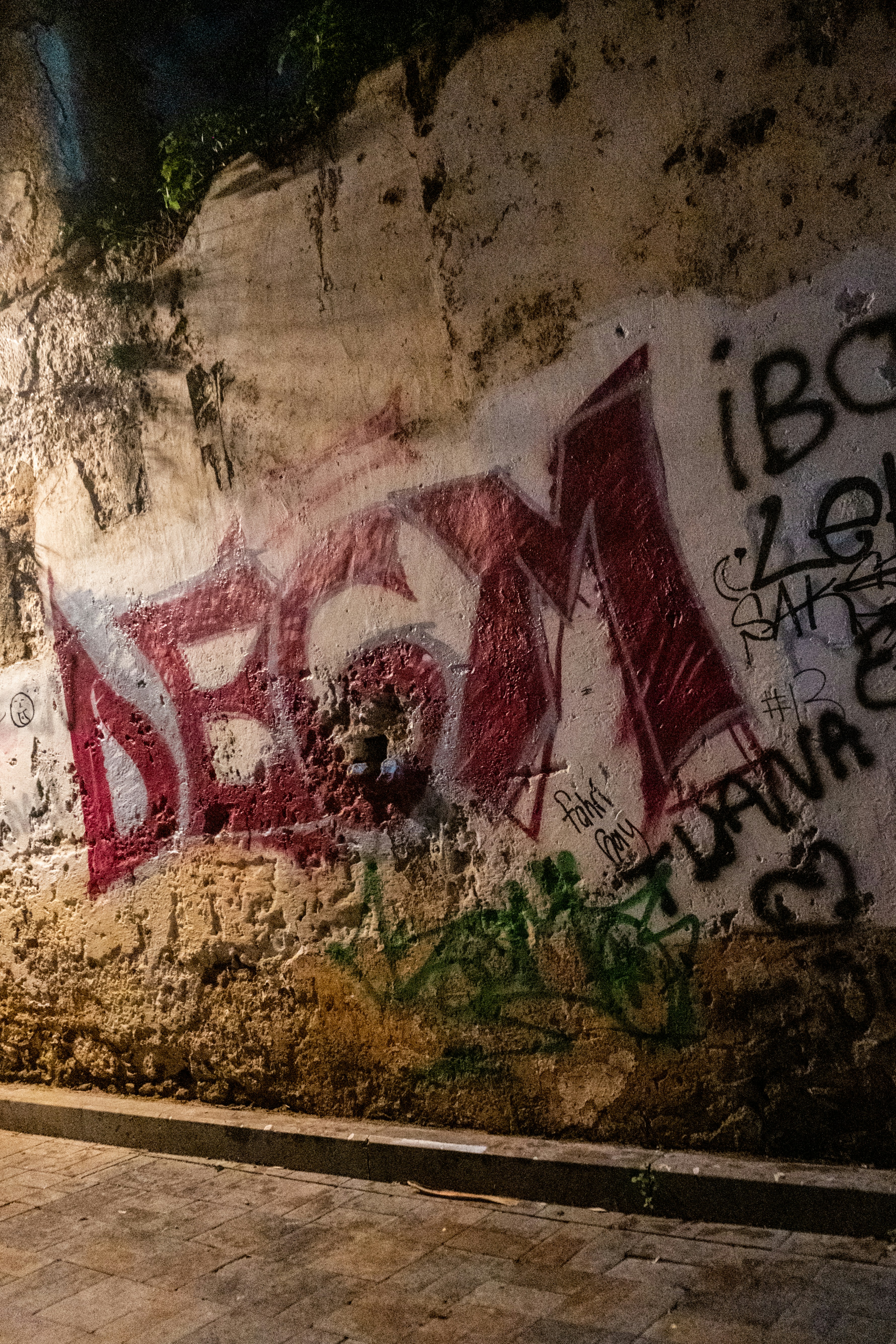 Cracked Concrete Canvas: Red Graffiti Amid Weathered White Wall