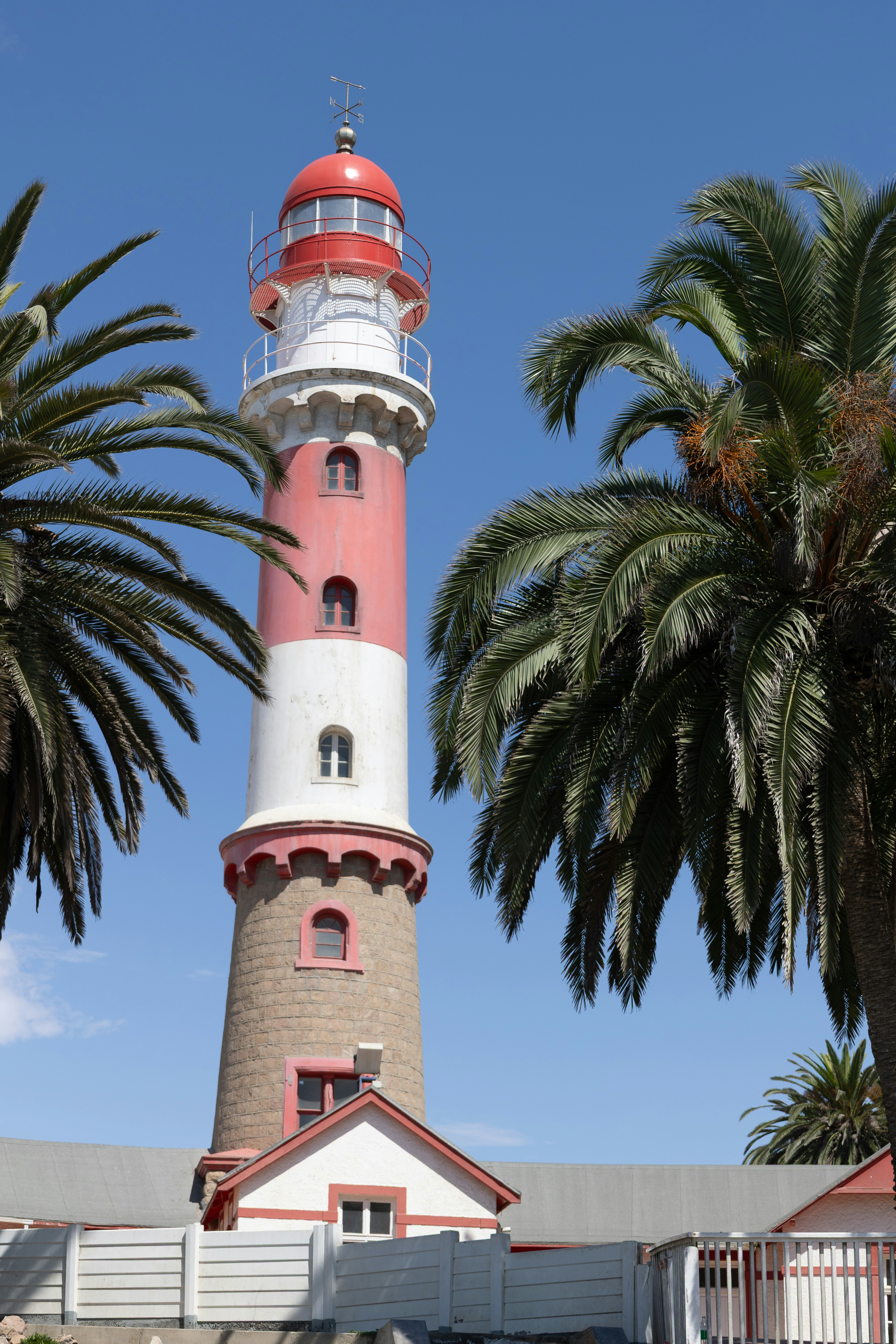 Lighthouse in bloom of palm shadows under a clear blue sky