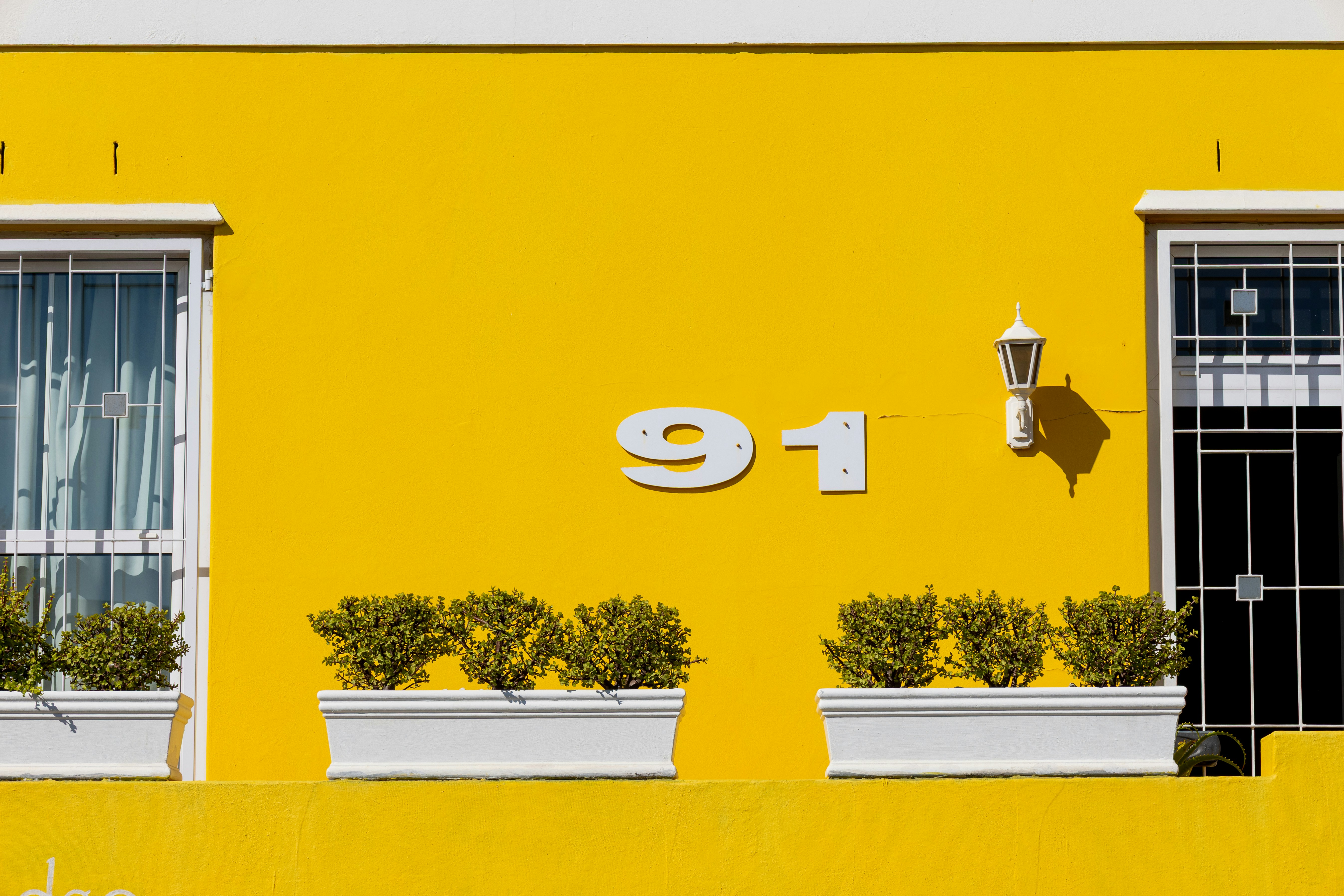 Yellow Facade with White Numerals: Symmetrical Plant Boxes under a Lantern