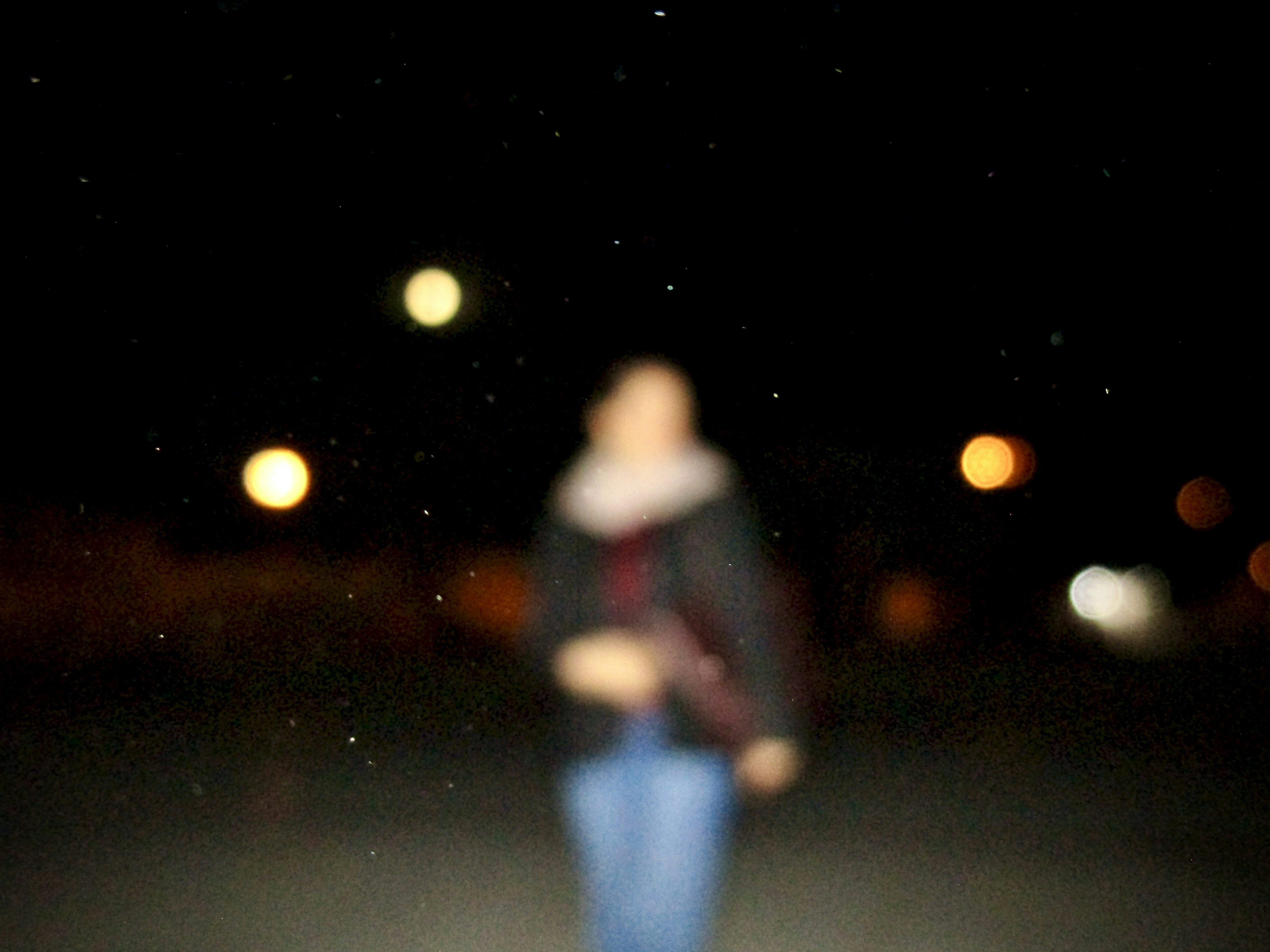 A blurry person stands in the dark with bokeh lights.
