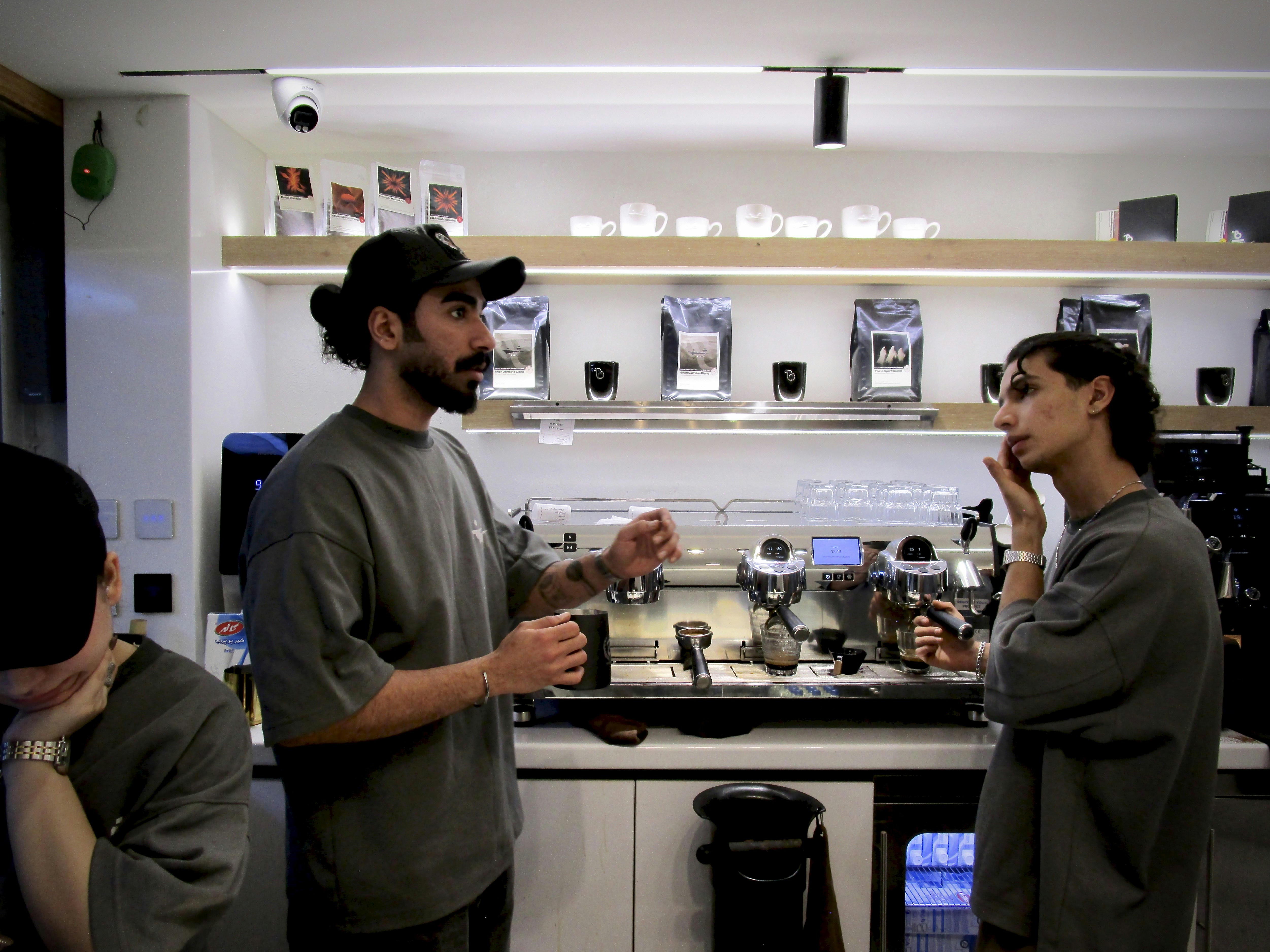 Two people talking behind a coffee machine counter.