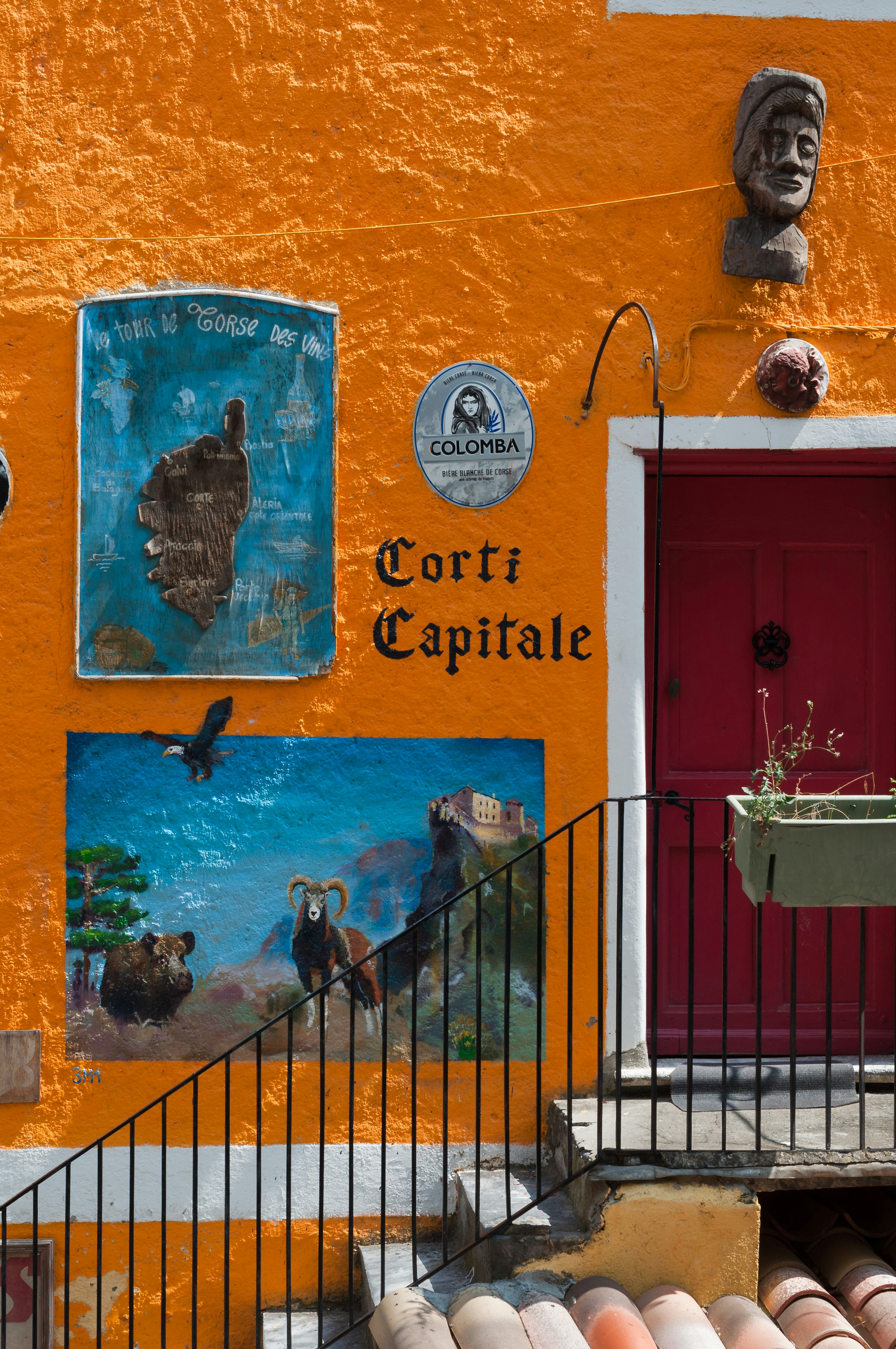 Cortis Capitales: a sunlit orange façade with murals and a crimson door