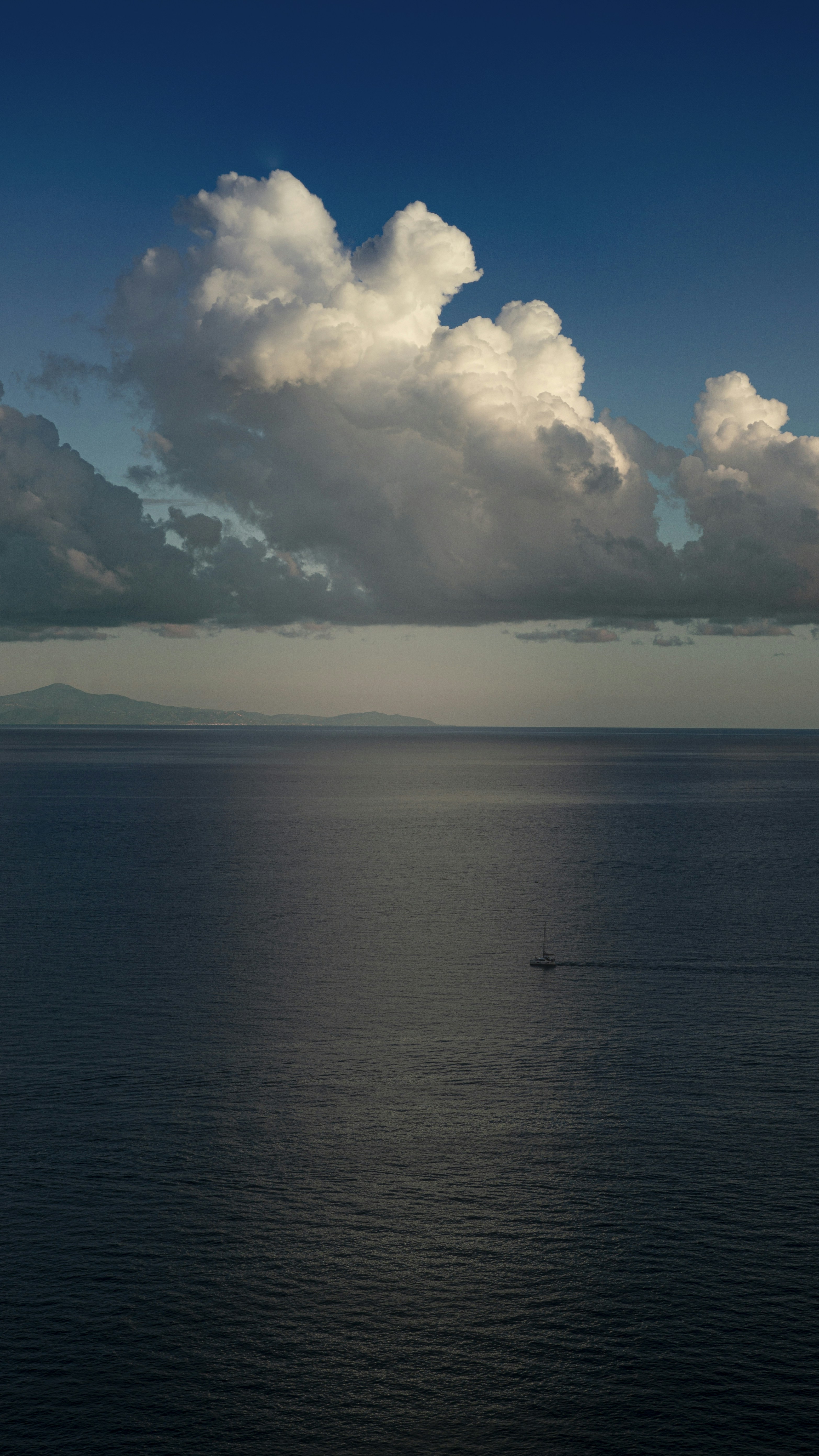 A solitary sailboat traces a silent wake beneath towering clouds