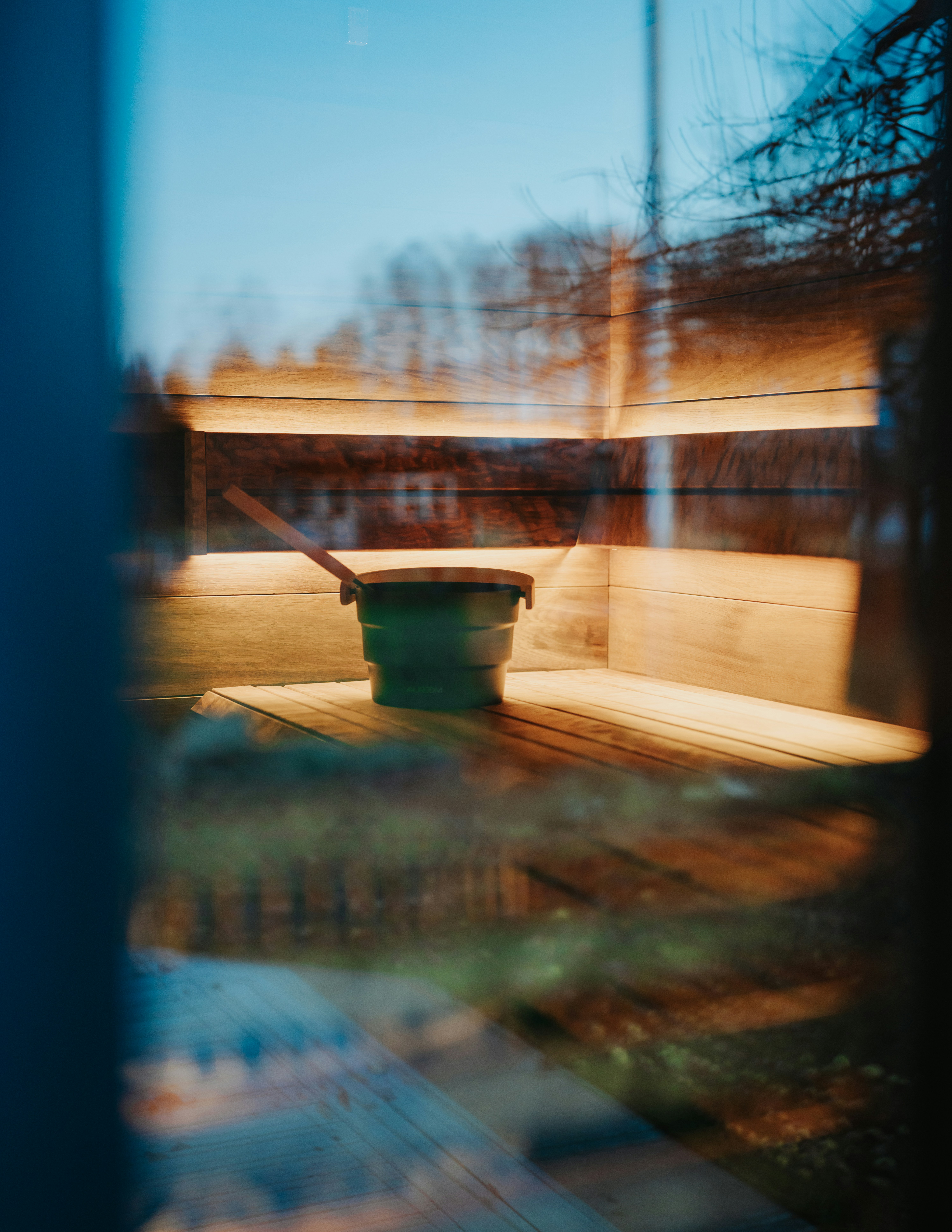 Green bucket on a sunlit wooden bench through a blurred window