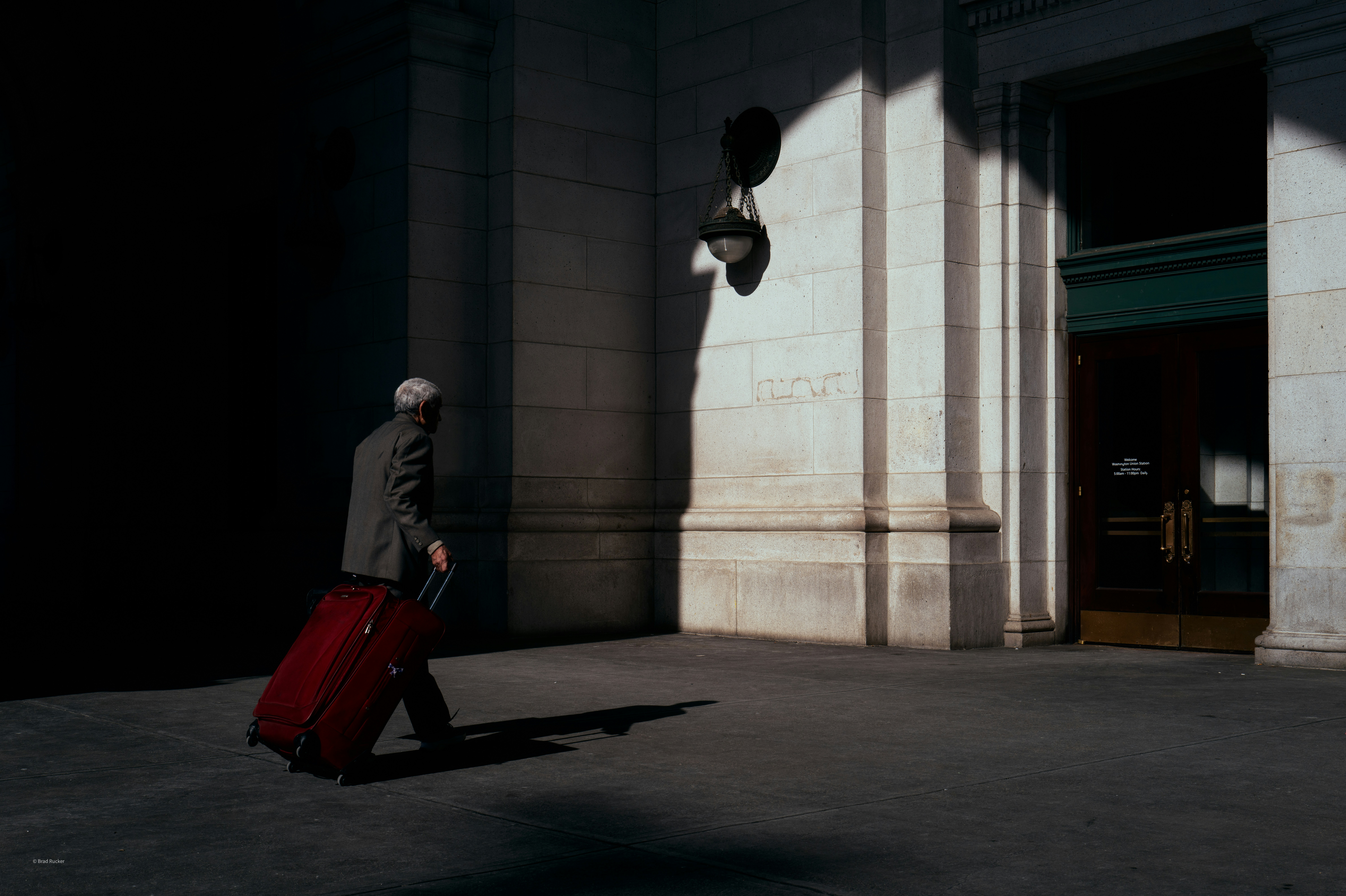Traveler with Red Suitcase Near a Sunlit Facade