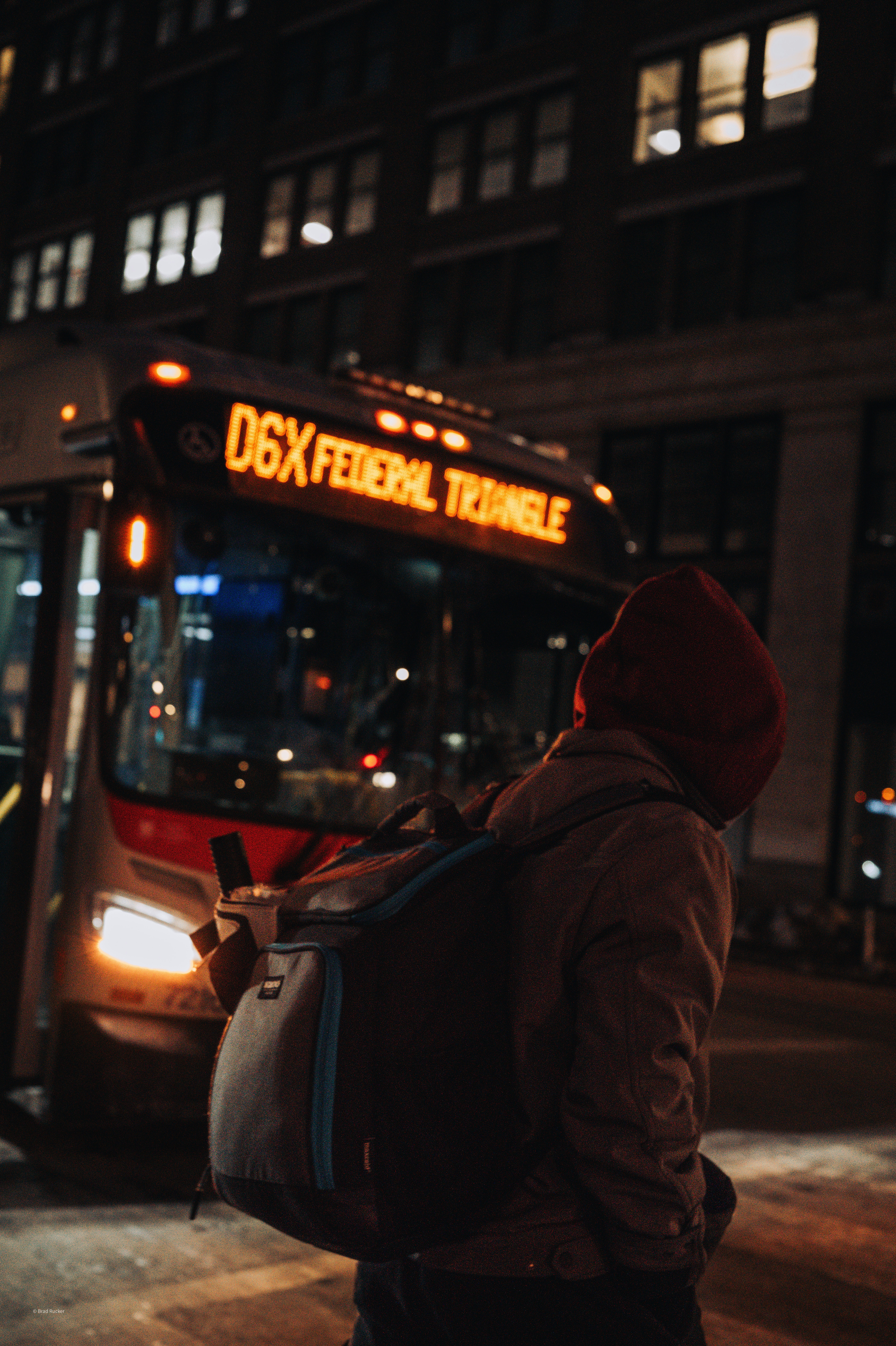 Backlit Commute: A Hoodie-Clad Traveler Buys Time at the Night Bus Stop