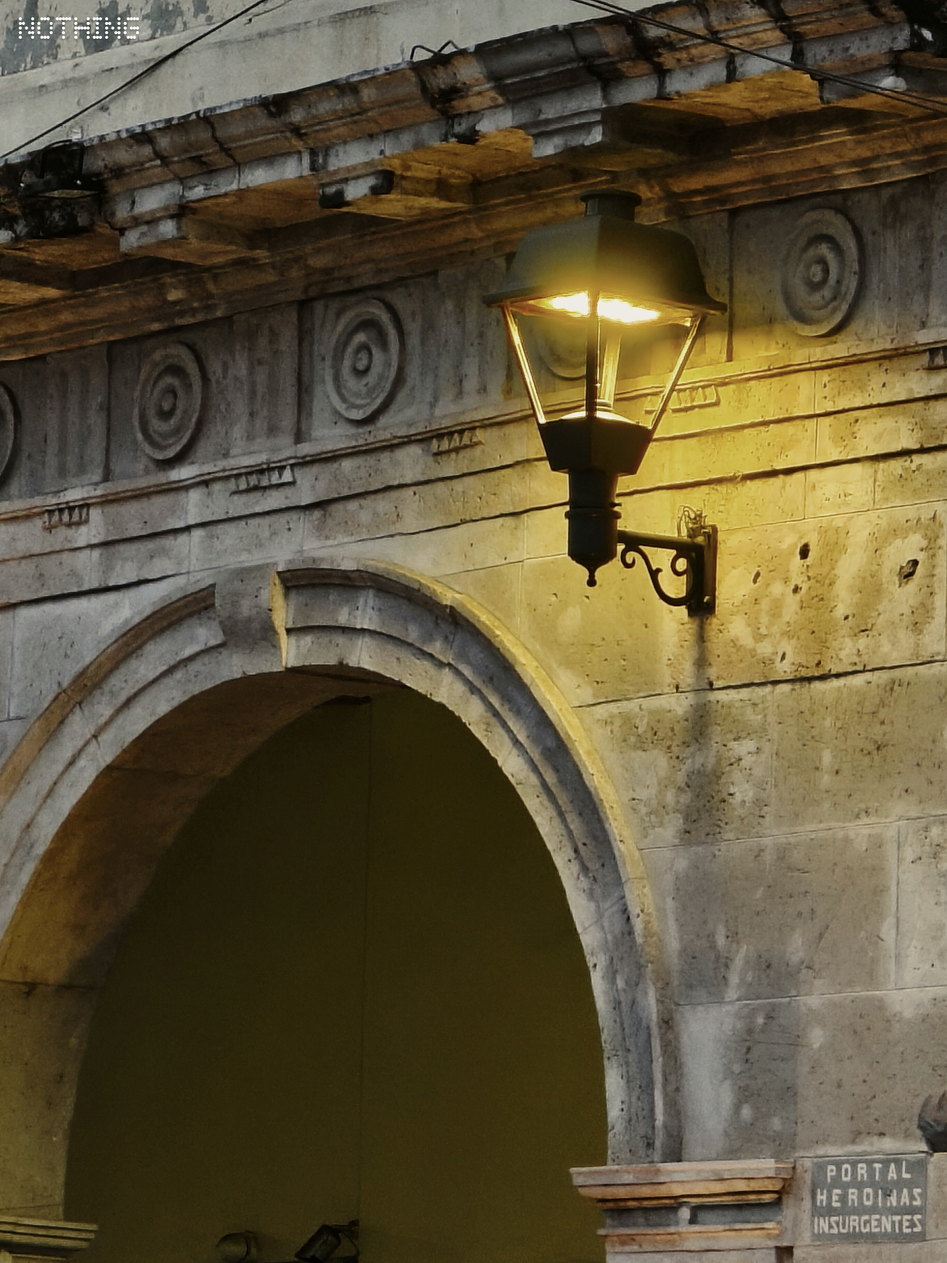 Old street lamp illuminates stone archway at night.
