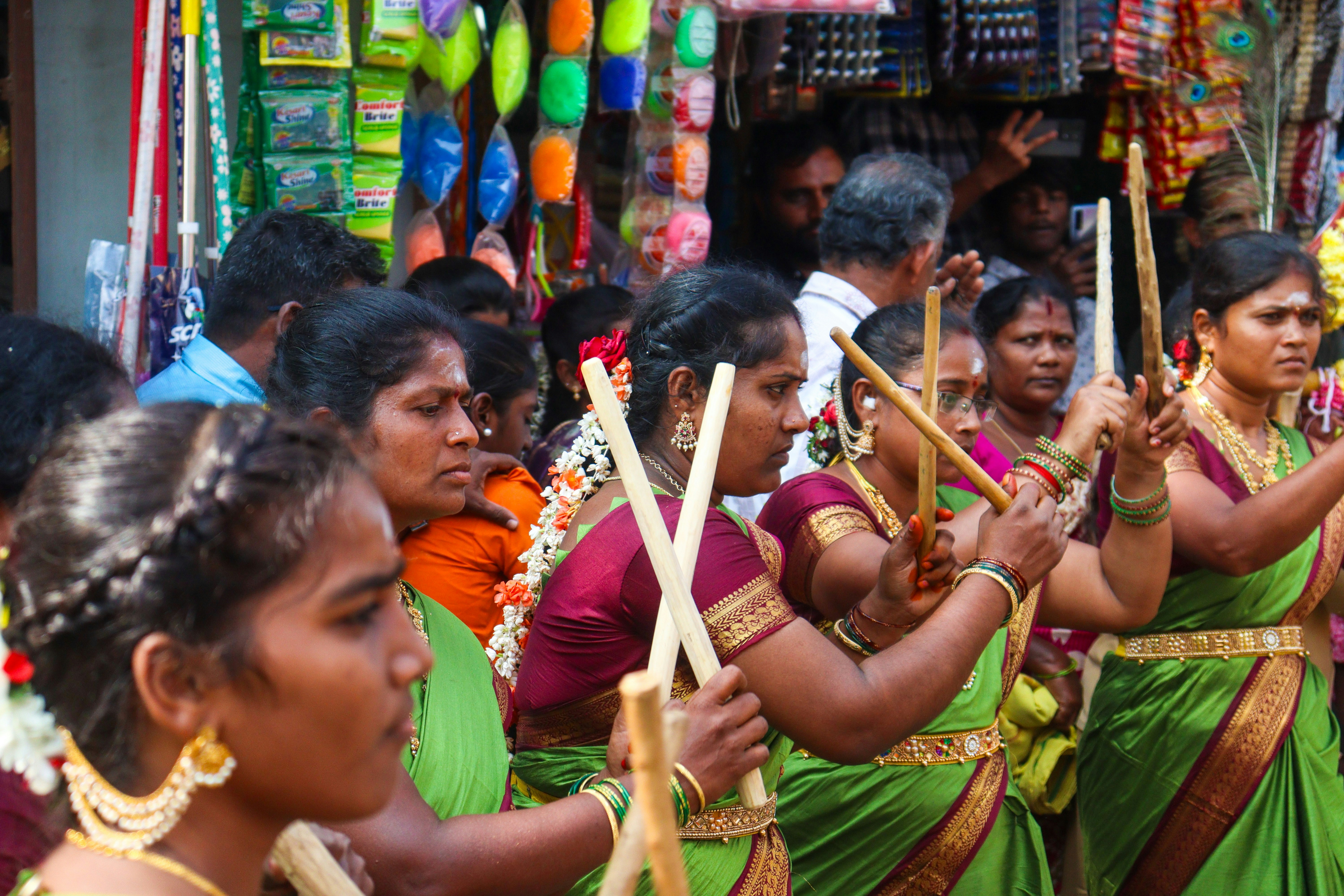 Women in vibrant saris raise wooden sticks in a busy market procession