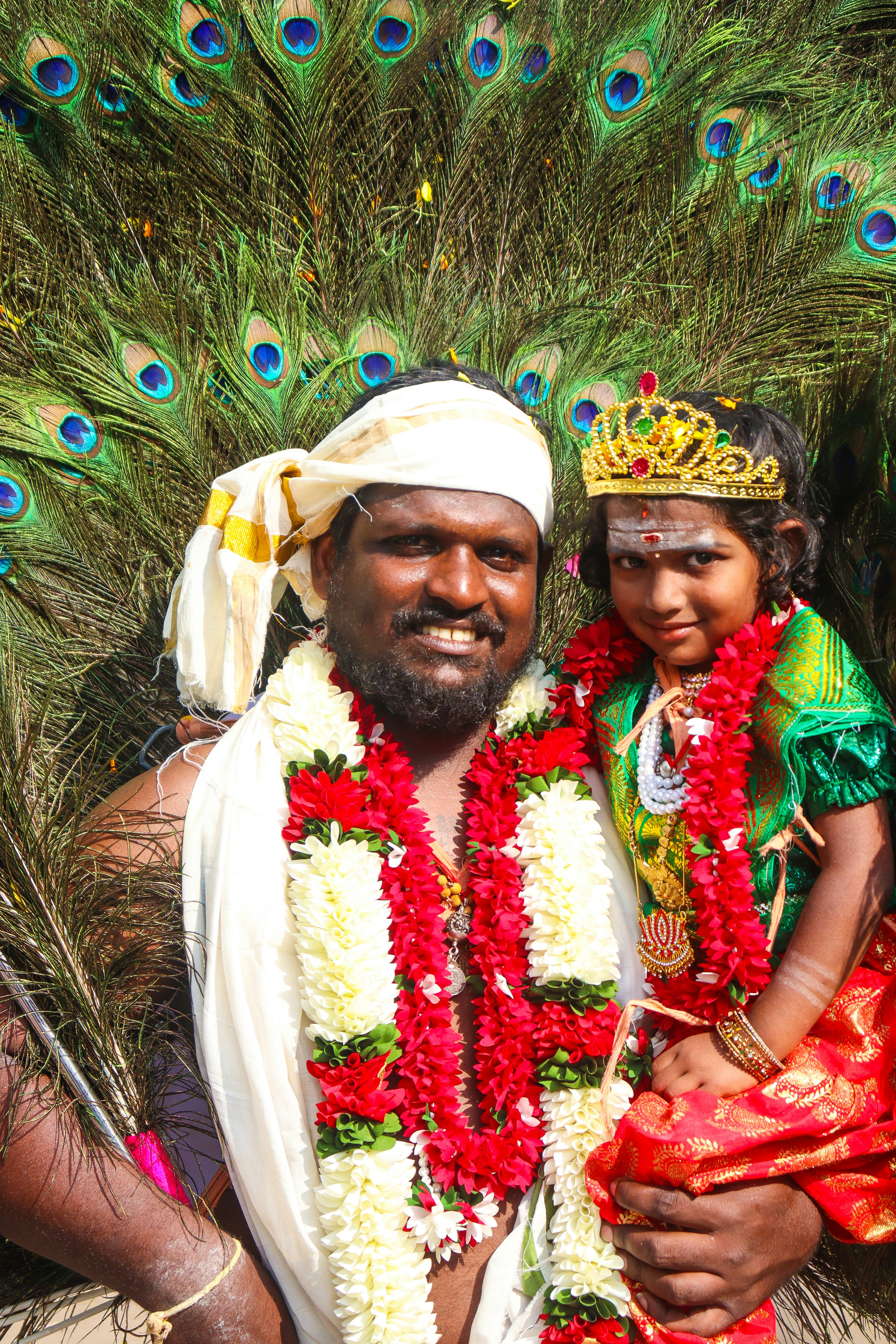 Garlanded Union: Father and Child Beneath a Peacock Canvas