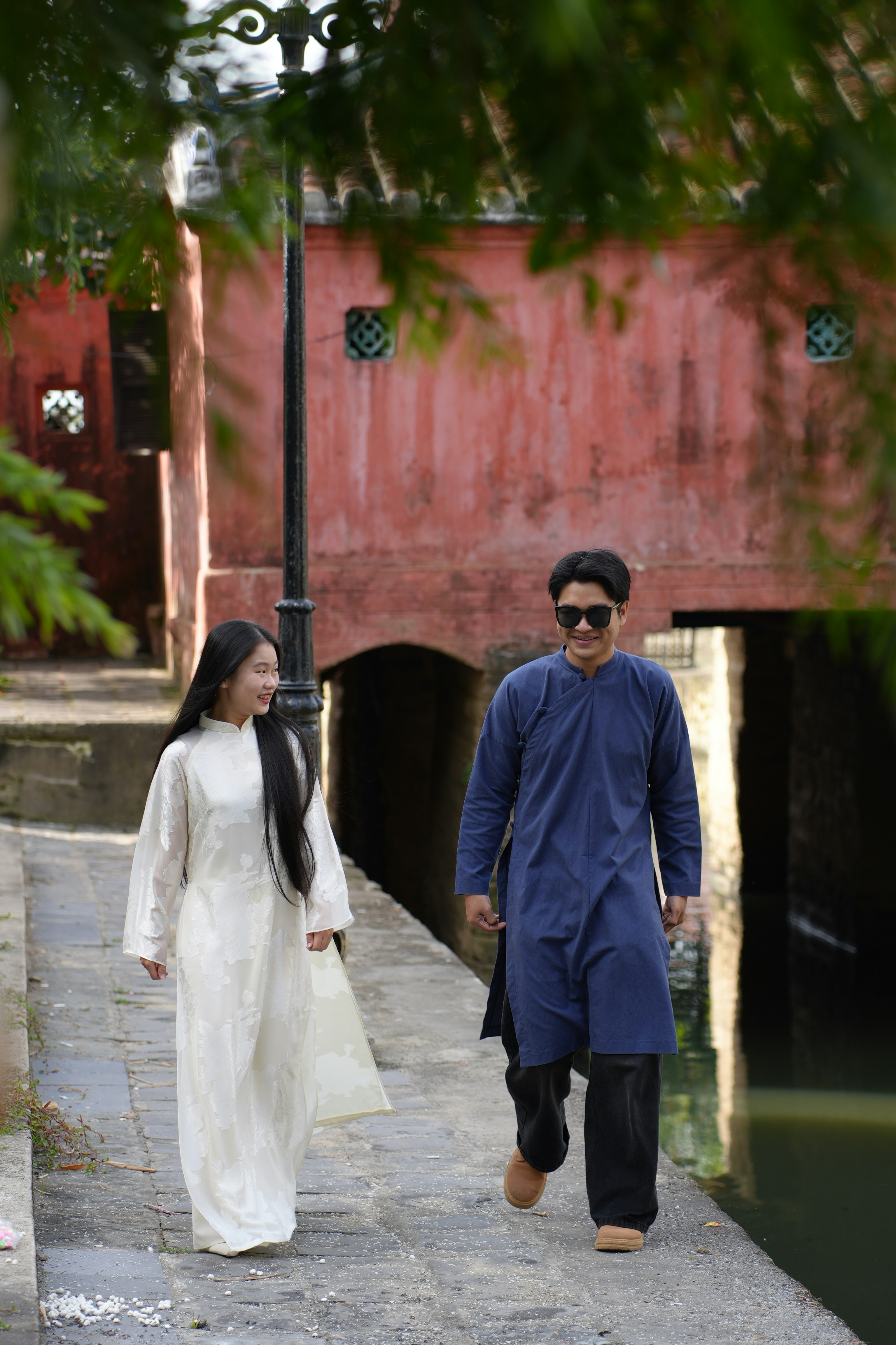 Quiet stroll by the red wall: a duo in traditional attire along a canal
