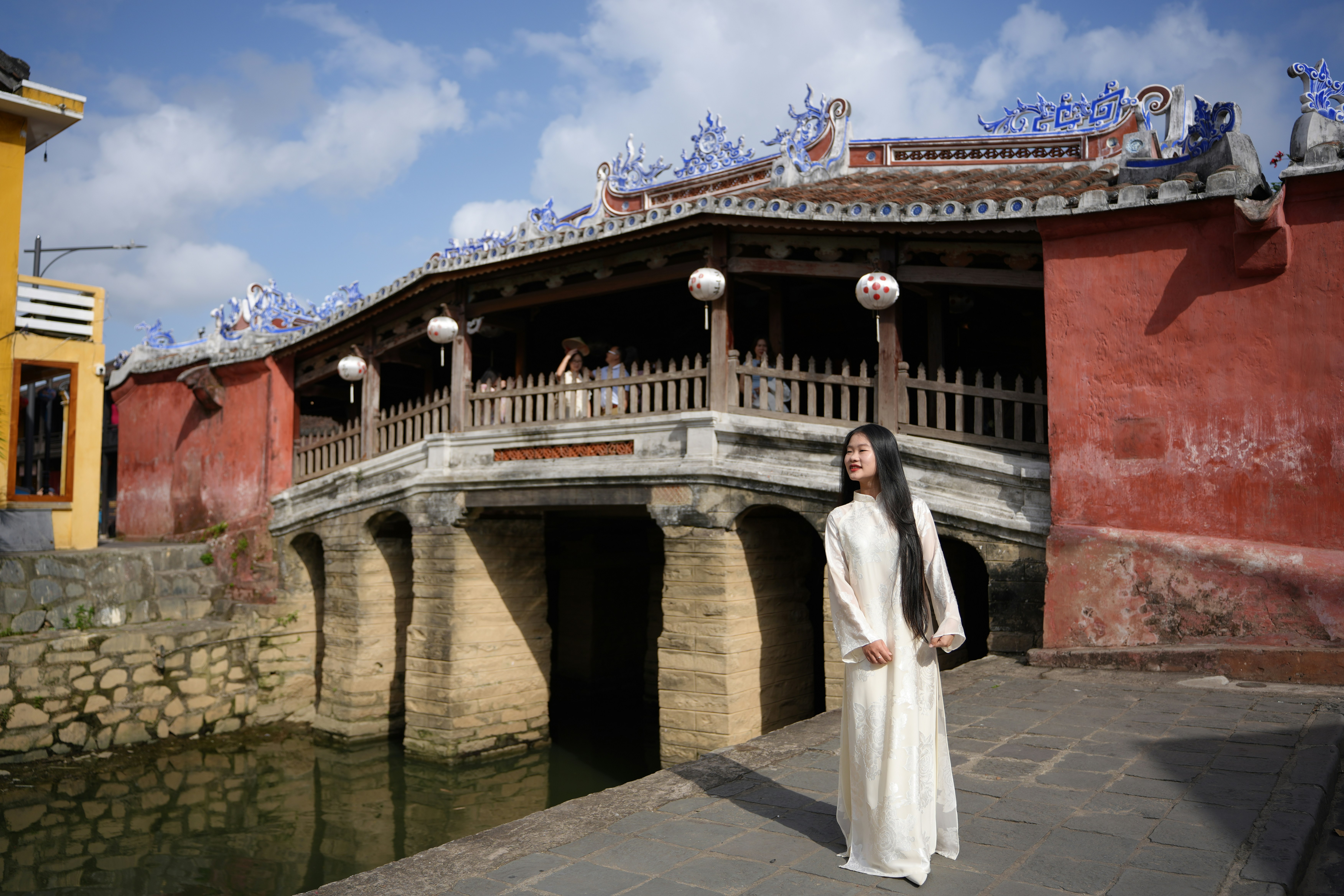 White-robed figure by a carved bridge under ornate temple eaves