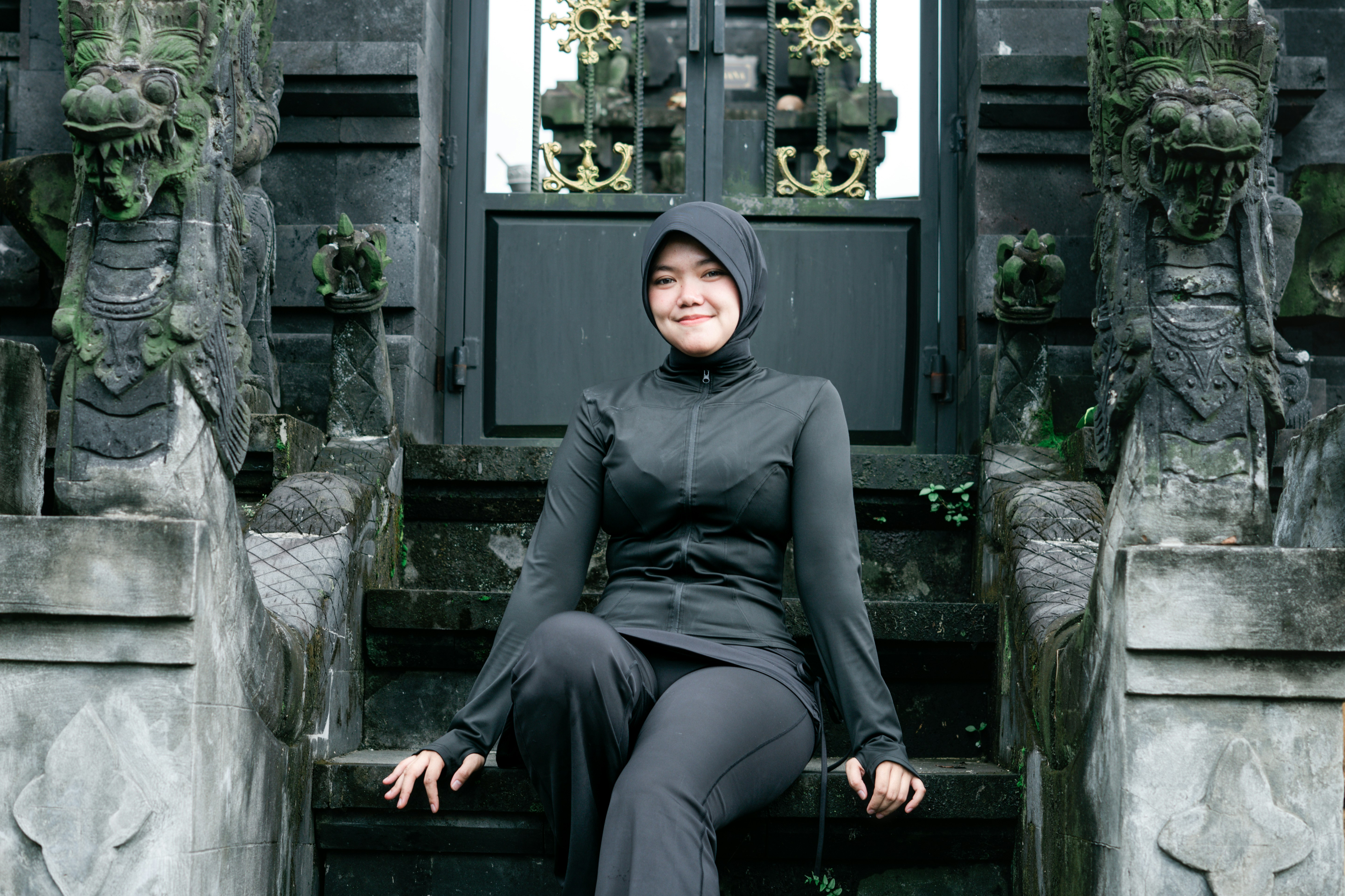 Woman in black hijab seated between stone guardians at temple gate