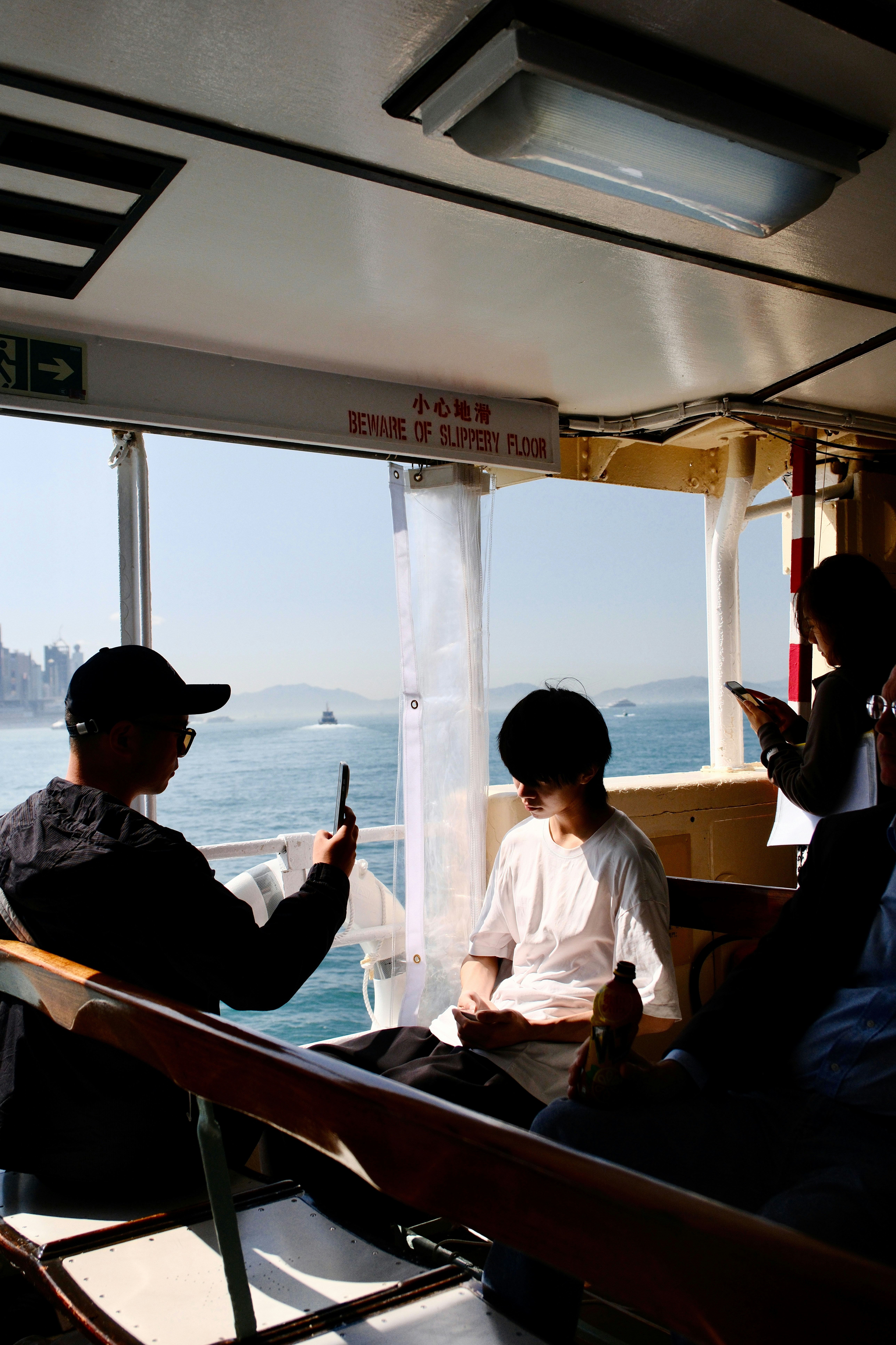 Sunlit ferry ride: passengers absorbed in screens as the sea glows beyond