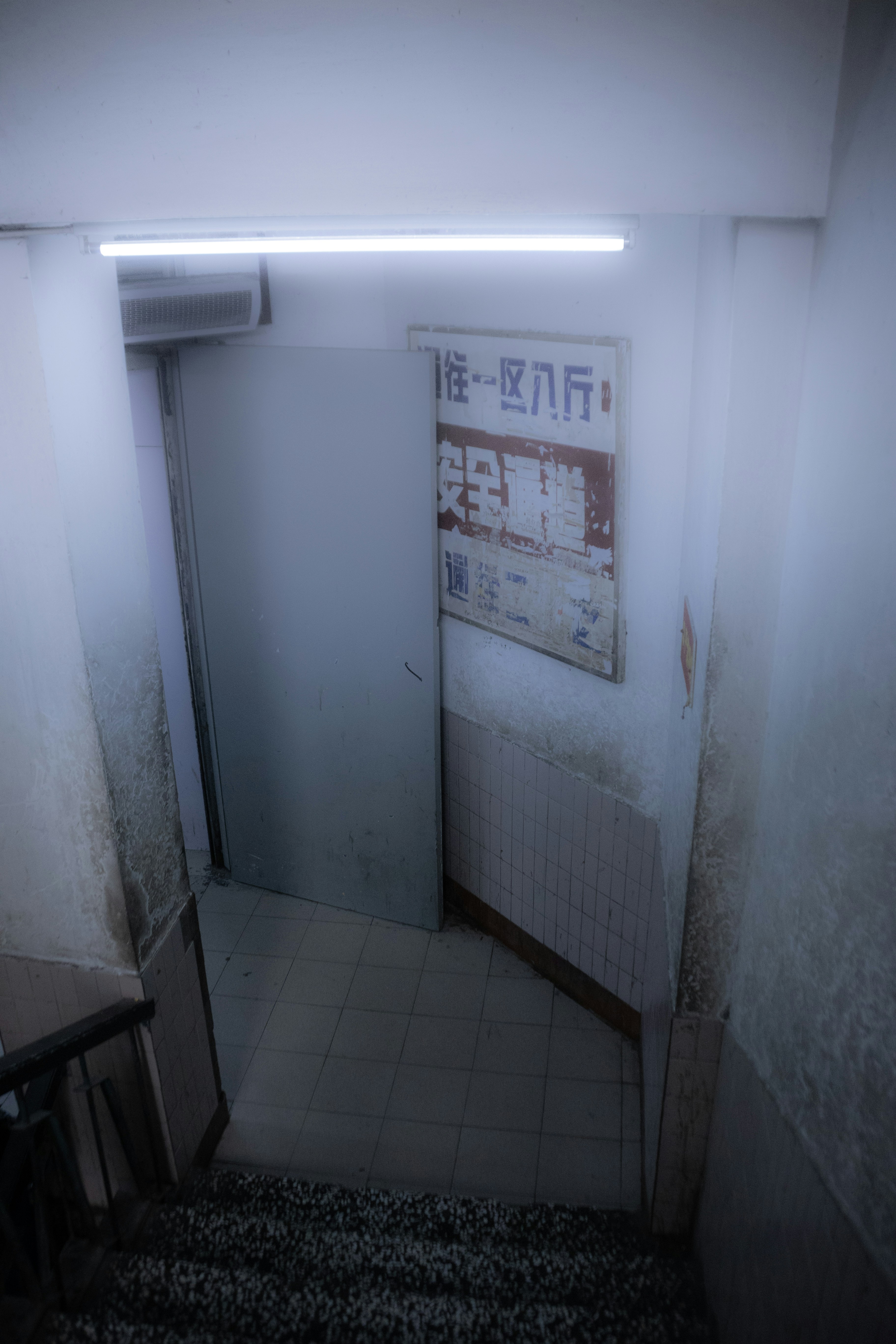Fluorescent Threshold: An Empty Stairwell Behind a Dim Sign