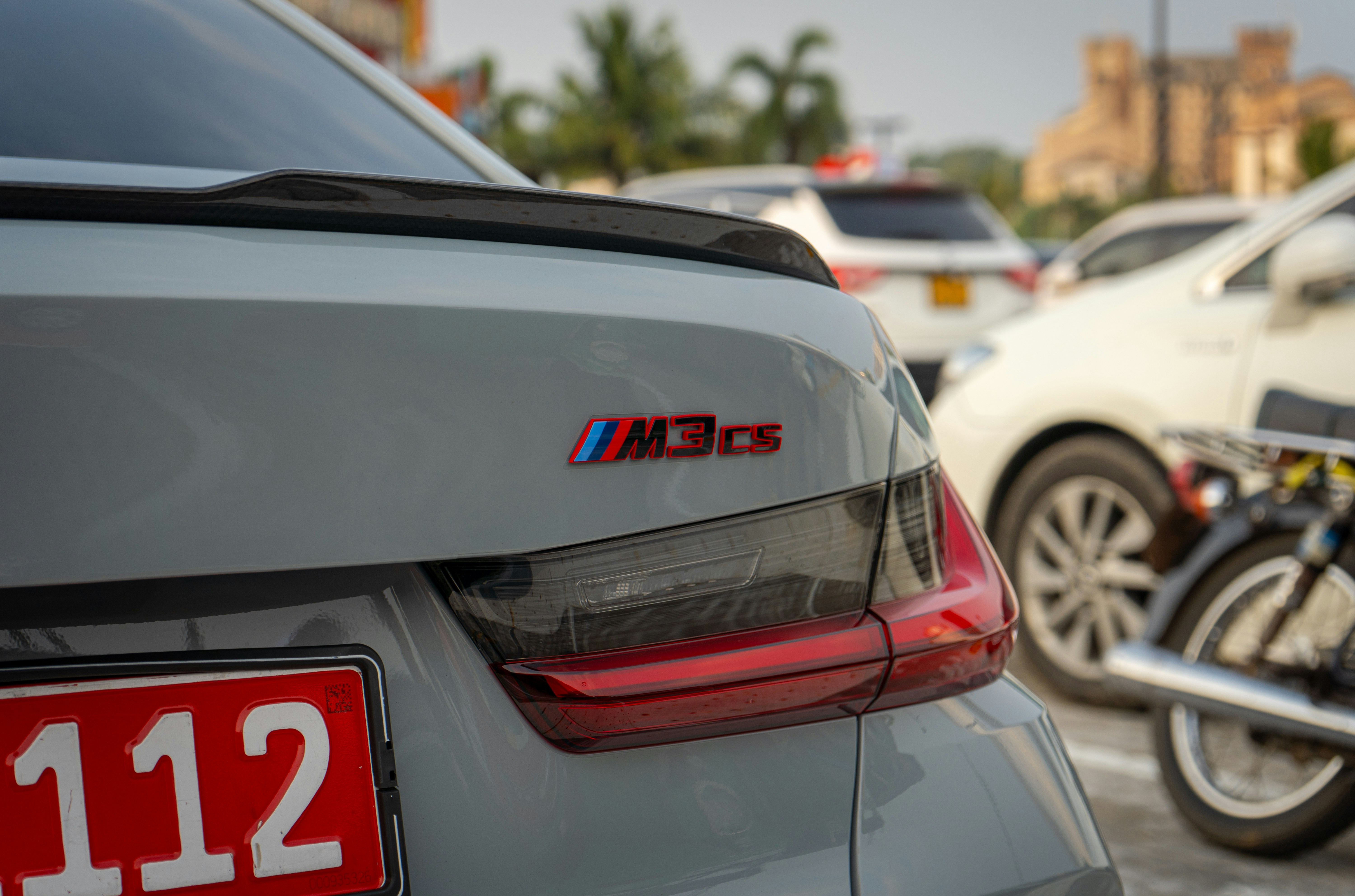 M badge and taillight silhouette: gray M3d badge on a compact rear quarter of a parked navigation-blue BMW