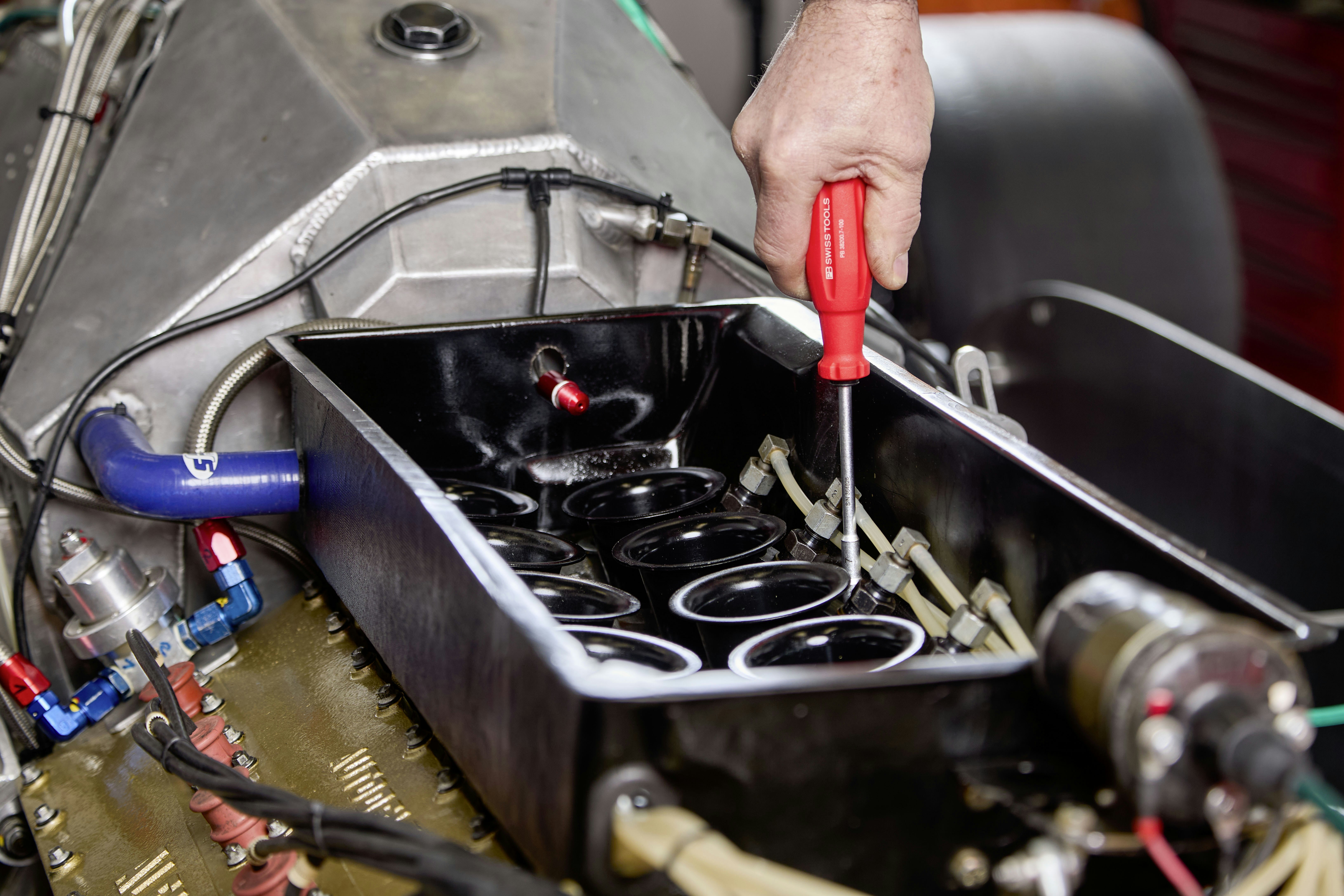 Mechanic using a screwdriver on car engine parts.