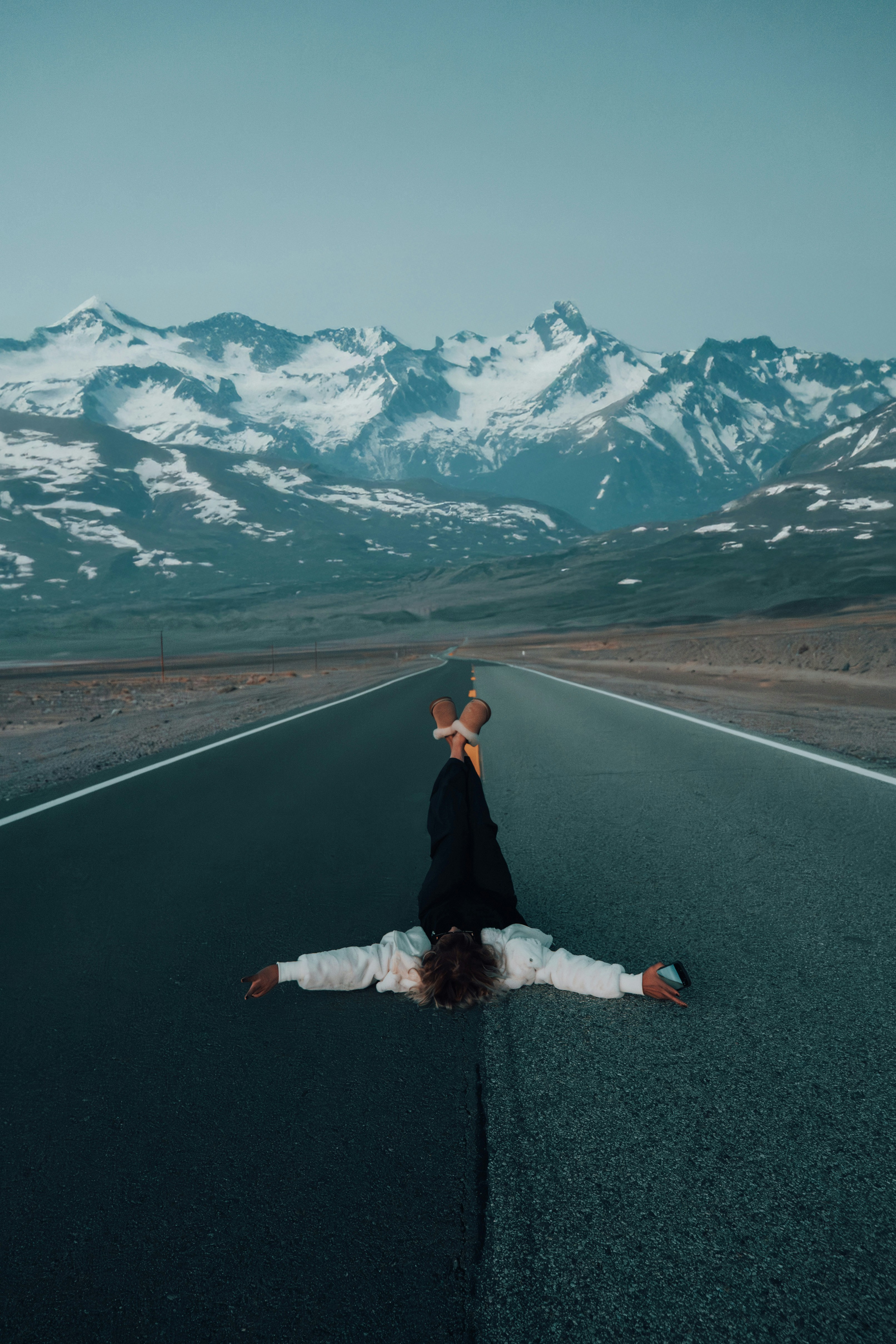 Person lying on a desolate road with mountains