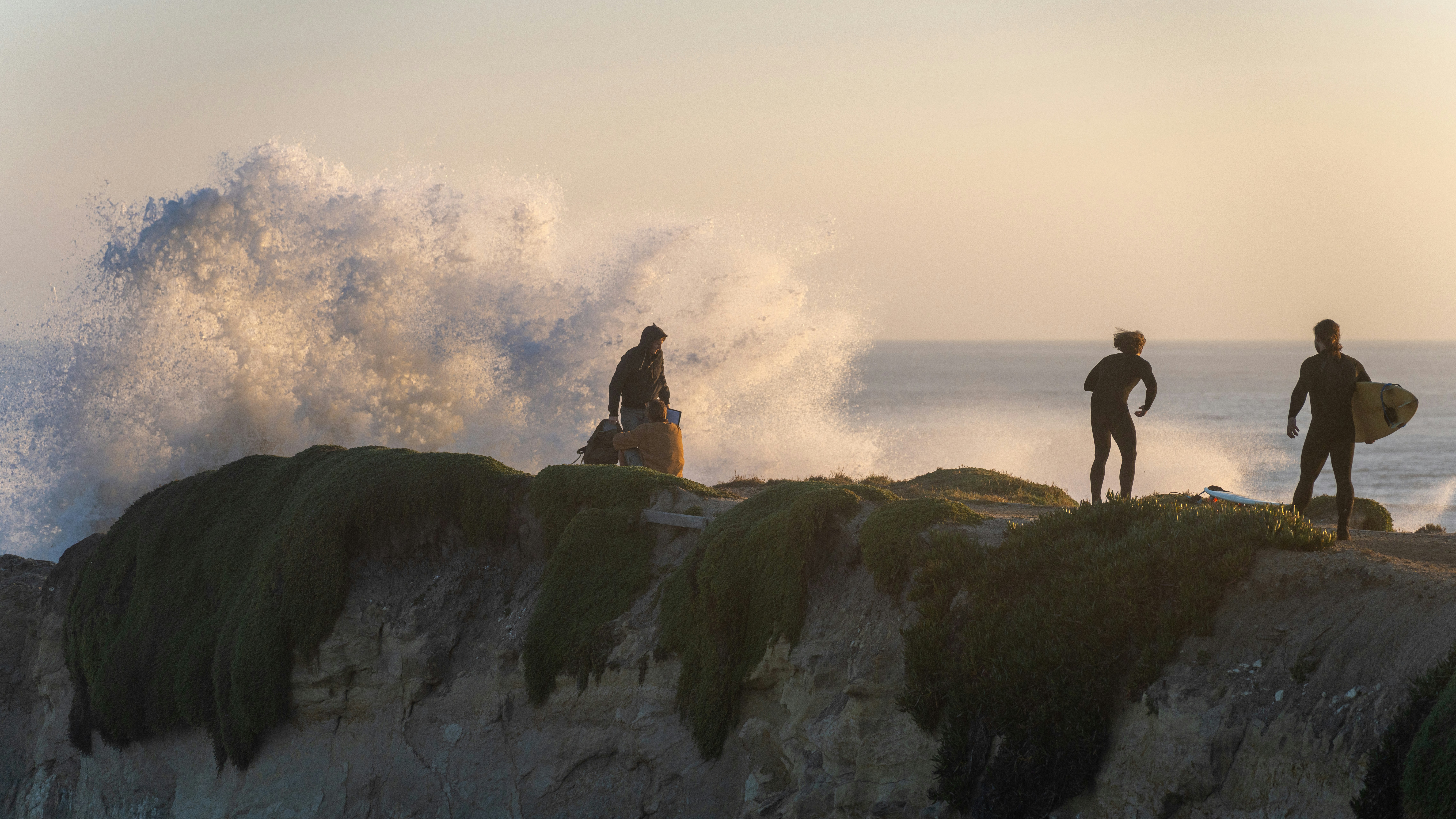 Surf silhouettes at sunset: surfers poised on a mossy cliff as a tidal wall rises