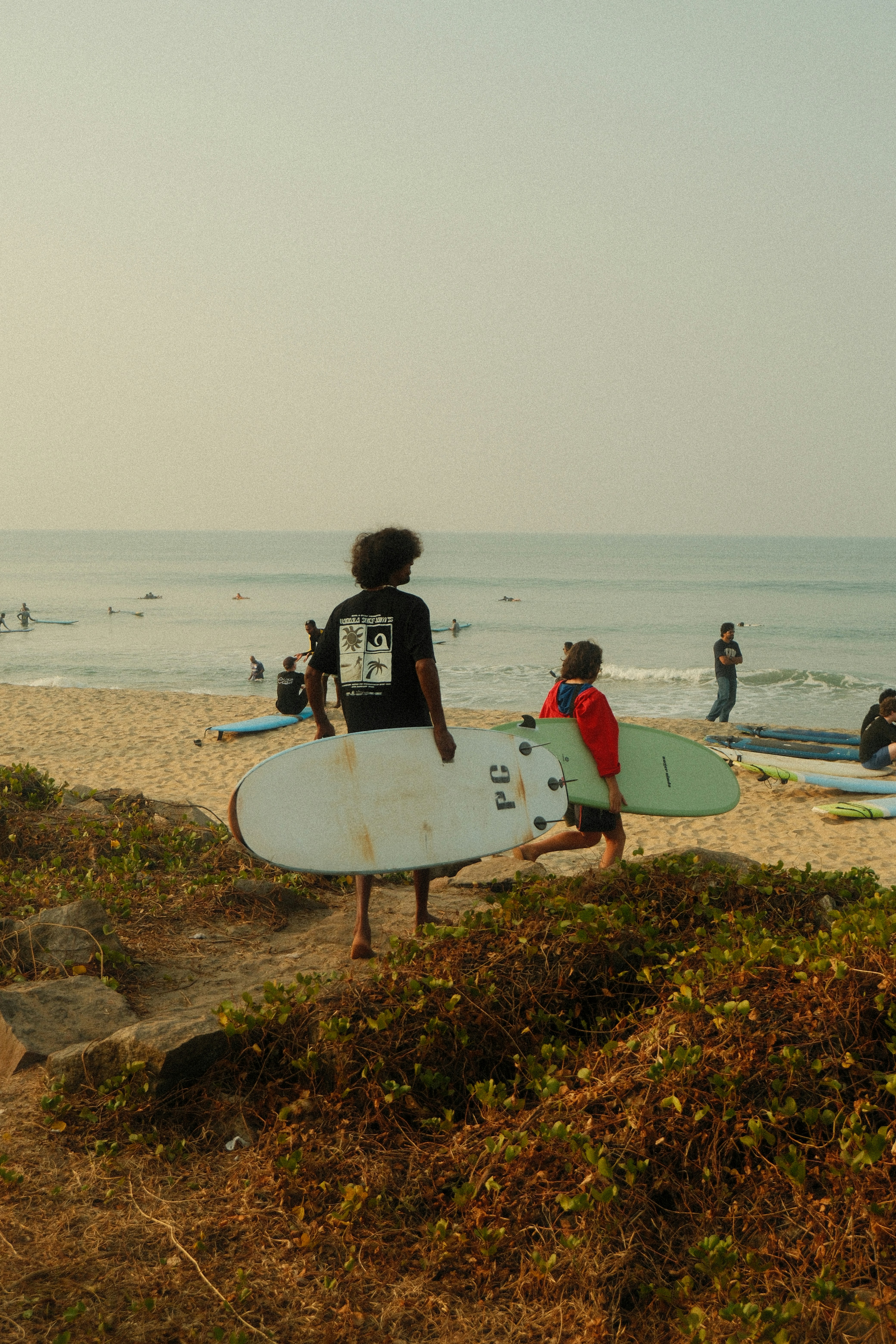 Surfer with whiteboard-streaked board returns from the tide, as beachgoers prep for session