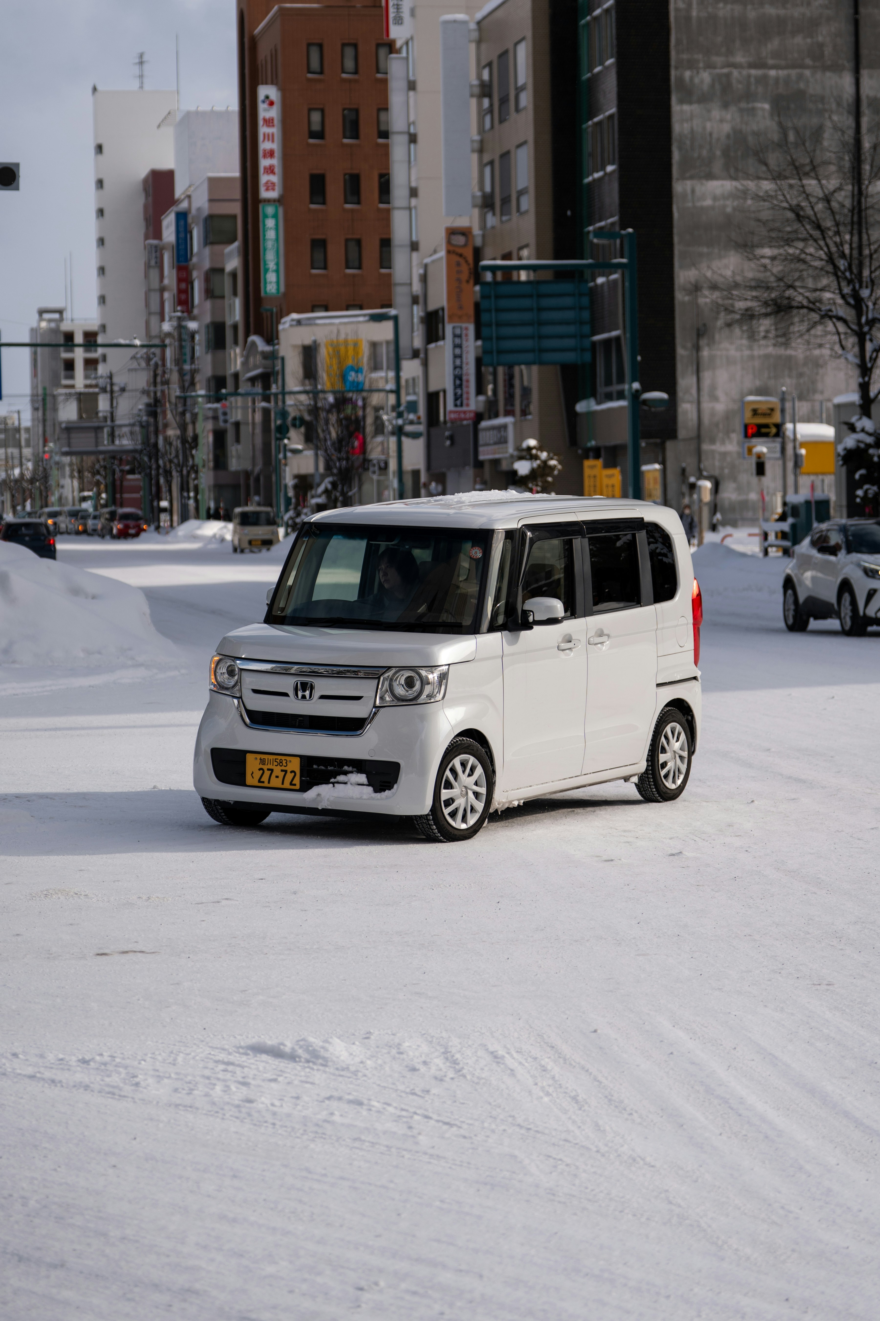 Snowbound City Courier: A white compact van navigates a frosty urban avenue
