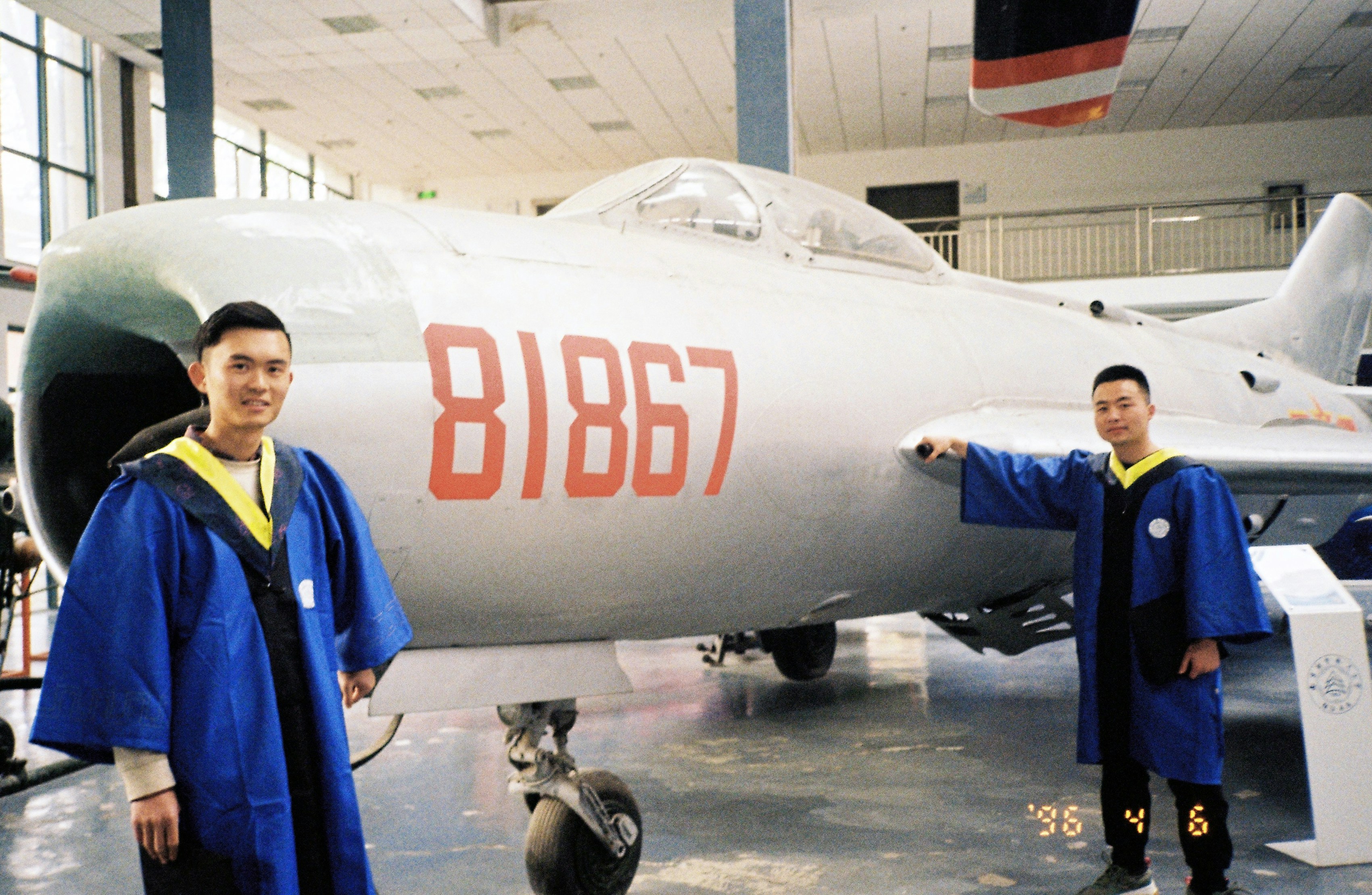 Two graduates pose beside a vintage jet in a museum hangar