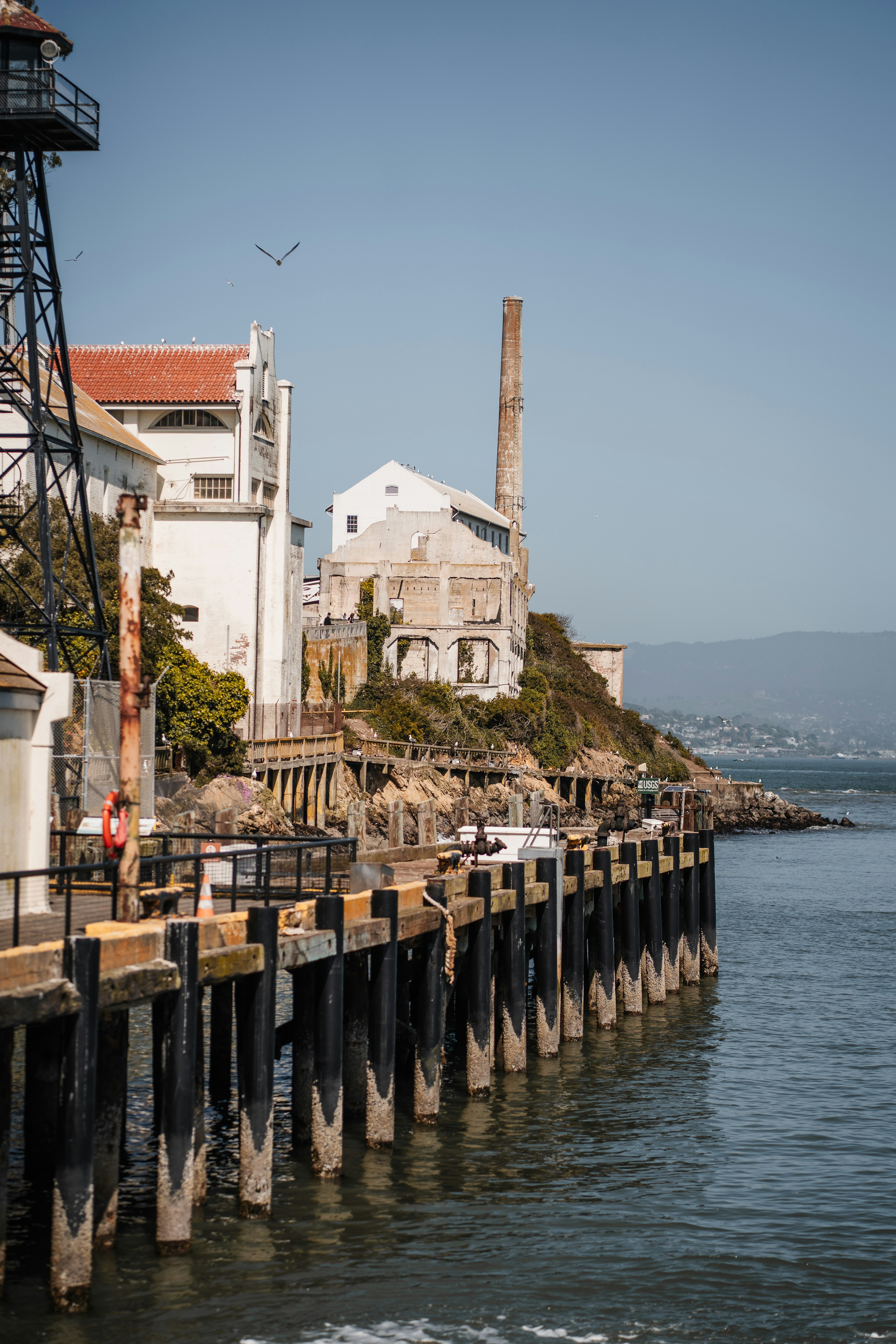 Harborfront ruin: sunlit industrial structures along a calm coastline