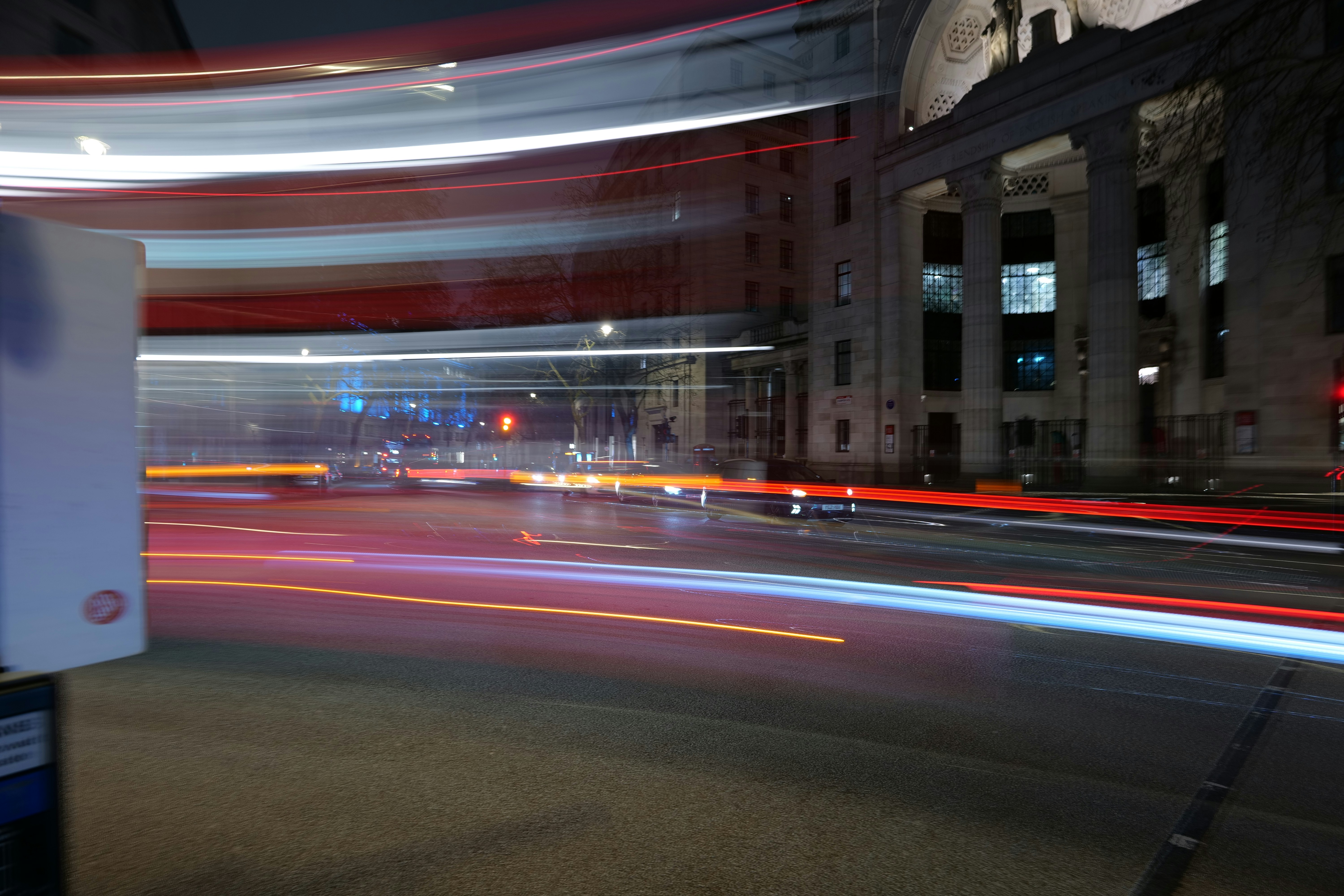 Long-exposure night street with neon light trails and architectural façade in the background.