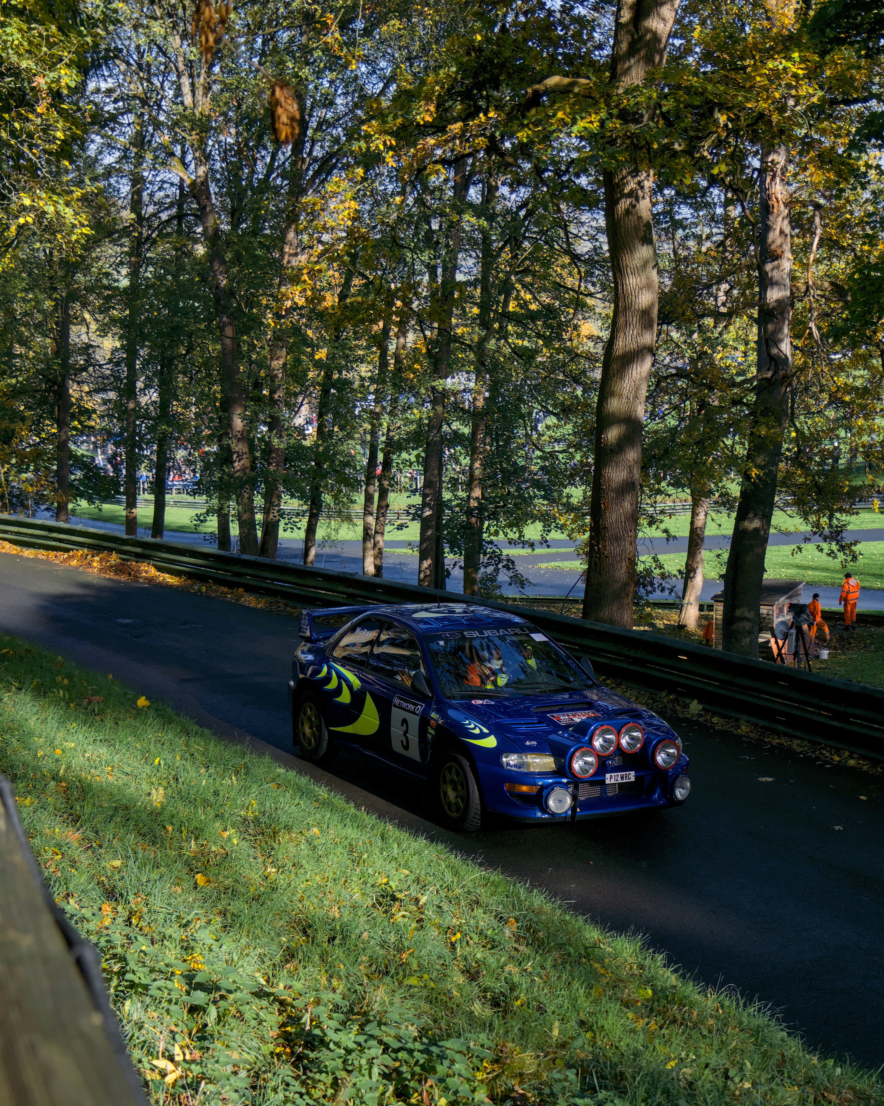 Blue rally car slicing through autumn sunlight on a winding forest road