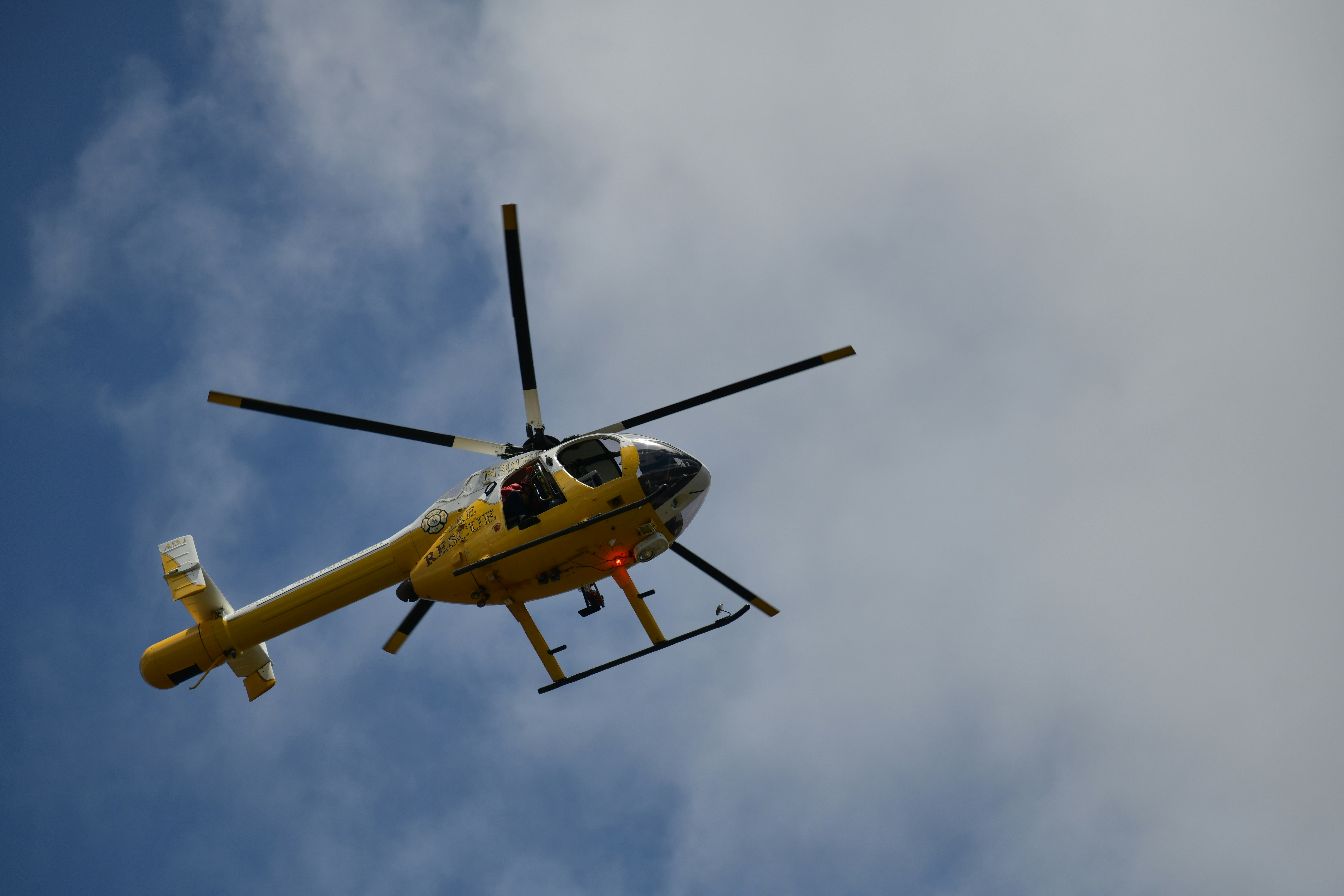 Low-angle Yellow Rescue Helicopter in Flight Against Cloudy Sky