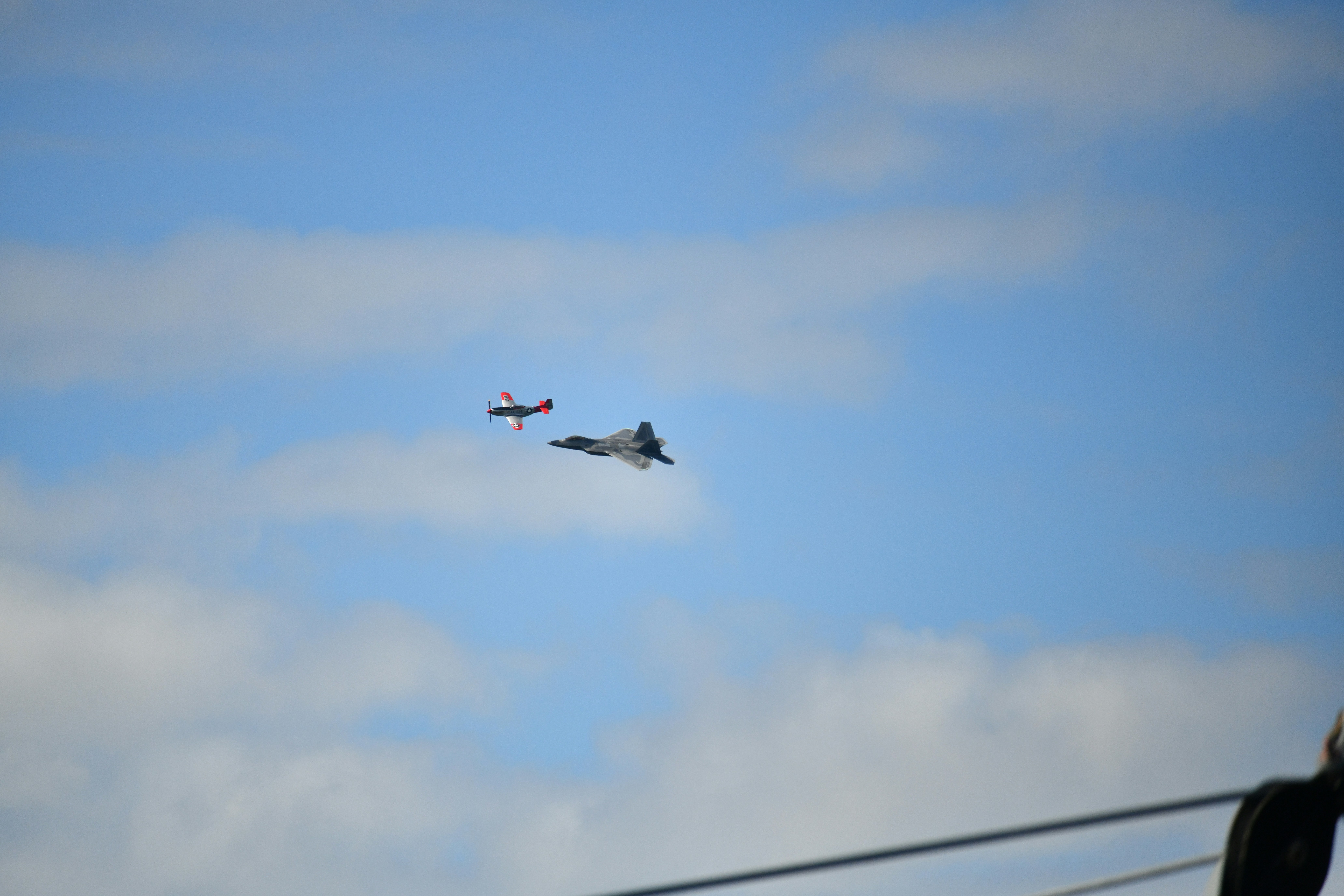 Sky Duel: Small aerobatic plane pursues a larger jet against a wispy cloud backdrop