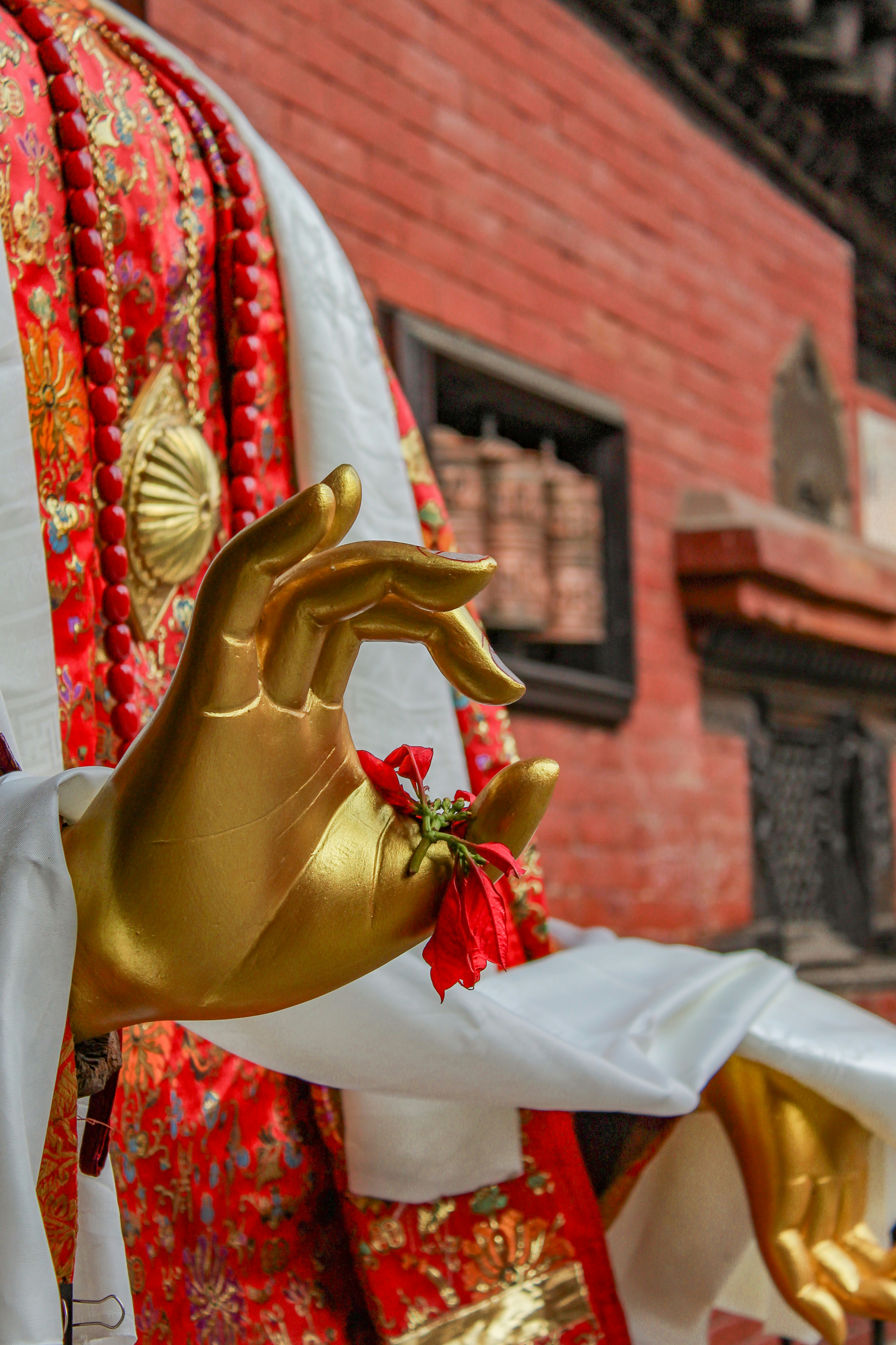 Gilded Gesture: A Sacred Hand Amid Red Robes and Brick