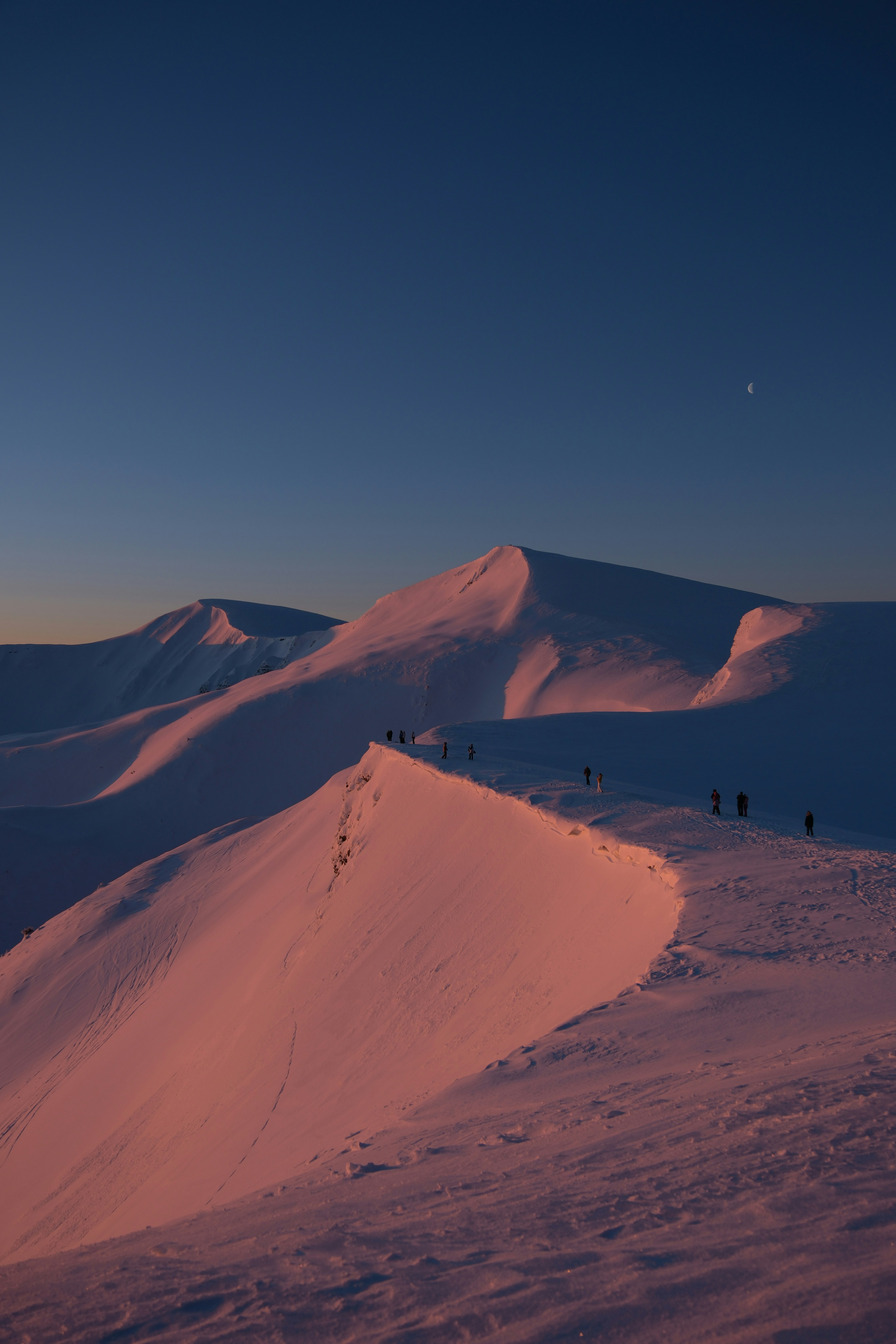Snowbound Ridge at Dusk: A Silhouette of Peaks Under a Crescent Moon