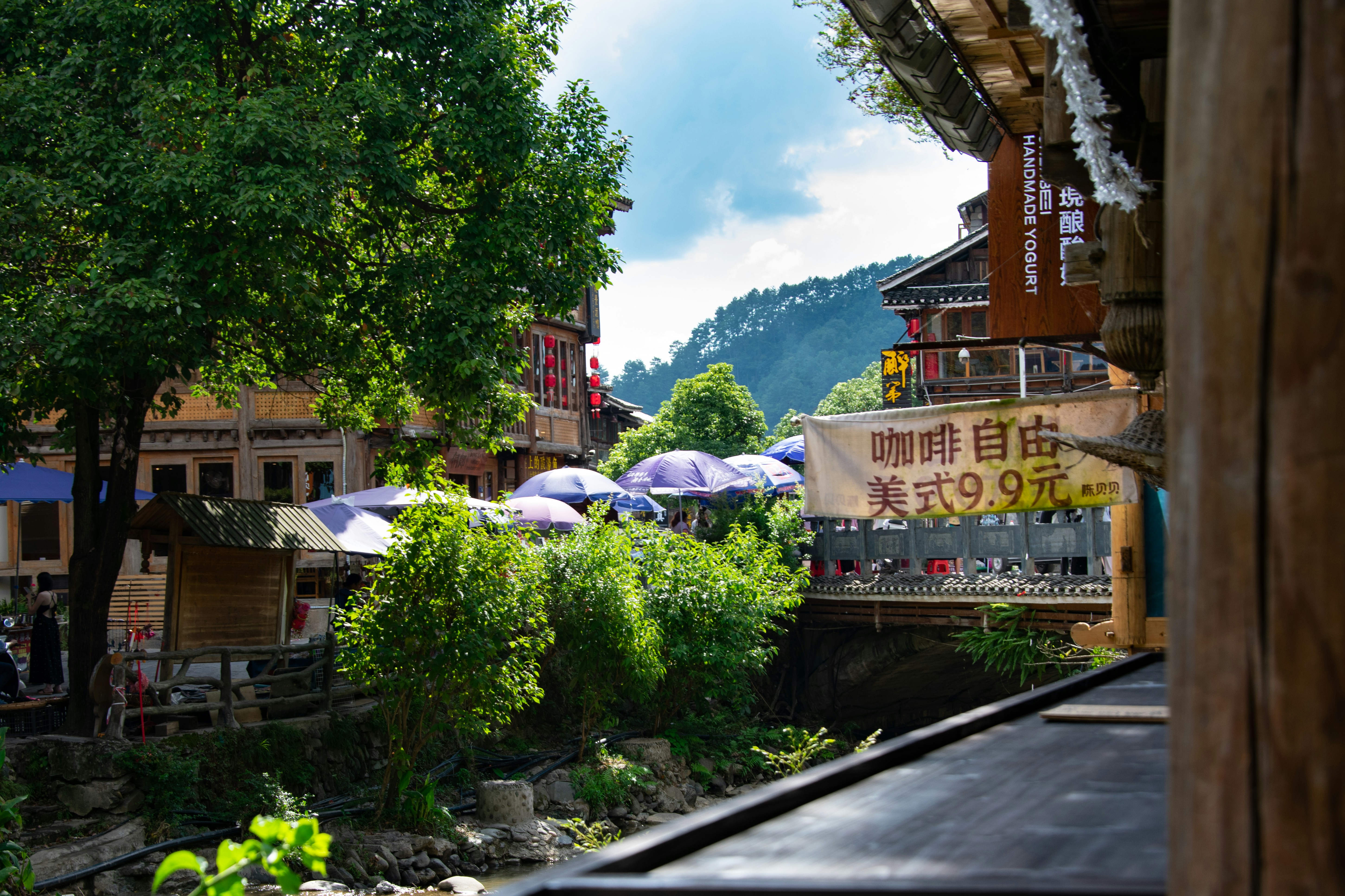 Sunlit riverside street with purple parasols and wooden architecture