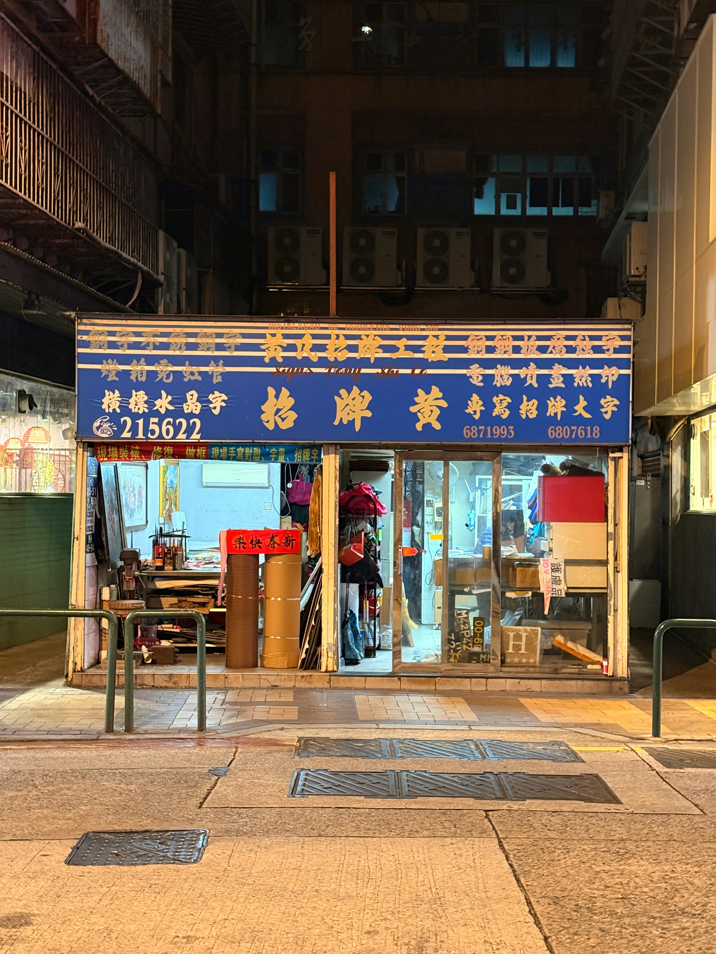 Blue Signage Over a Lantern-Lit Workshop Stall on a Narrow Urban Street