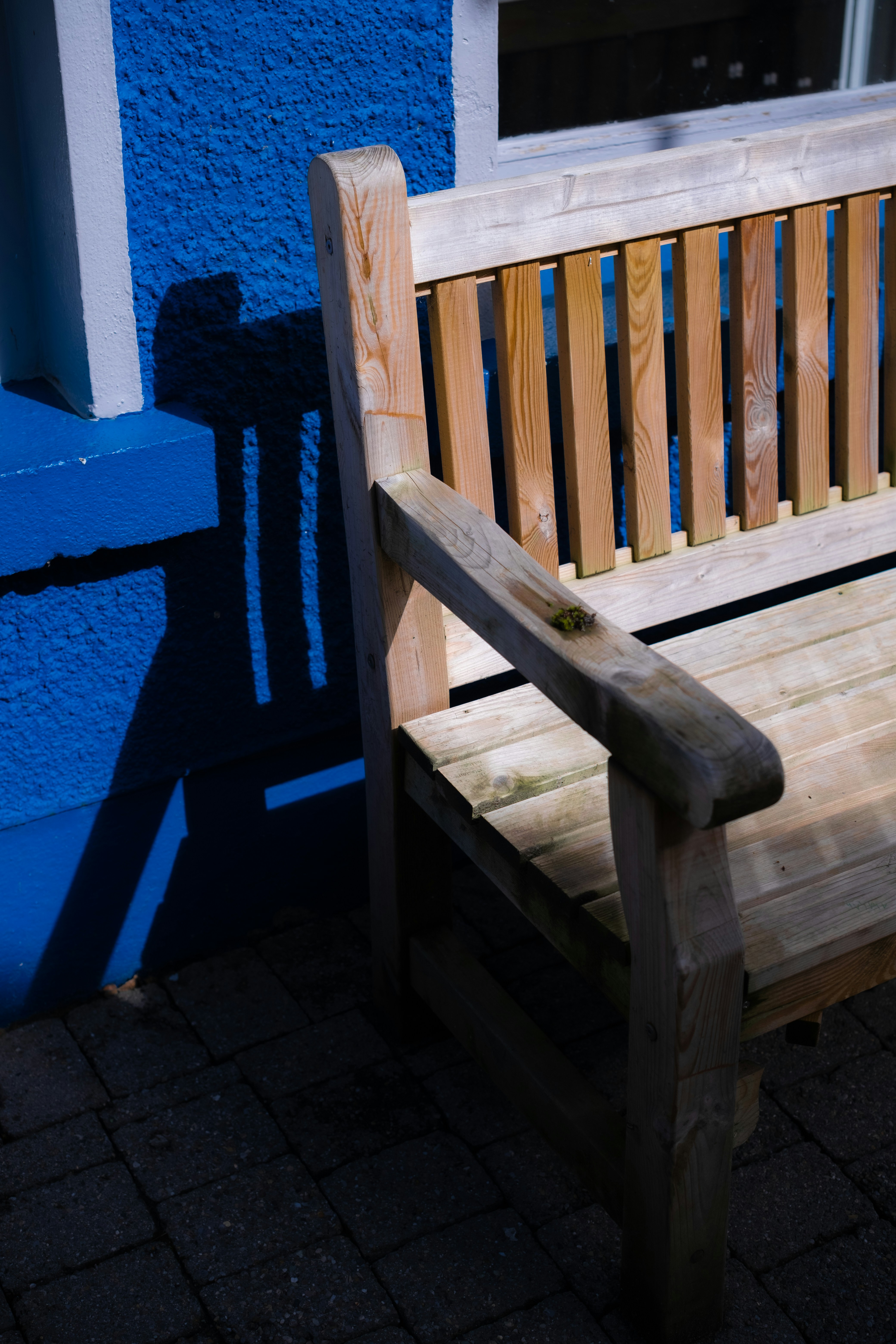 Shadowed Bench Beside a Bright Blue Wall