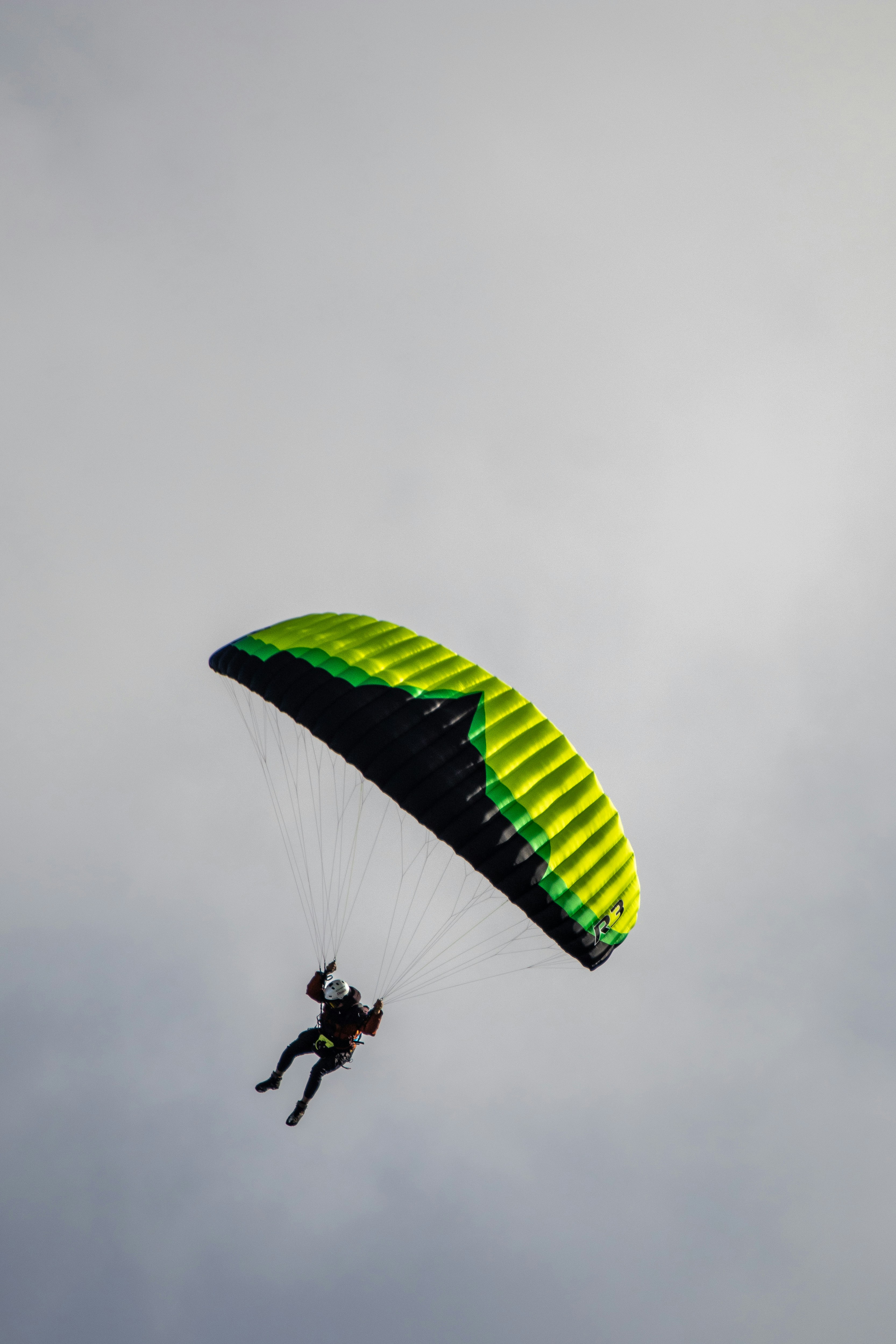 Bright Green-Black Paraglider Slice Against An Overcast Sky