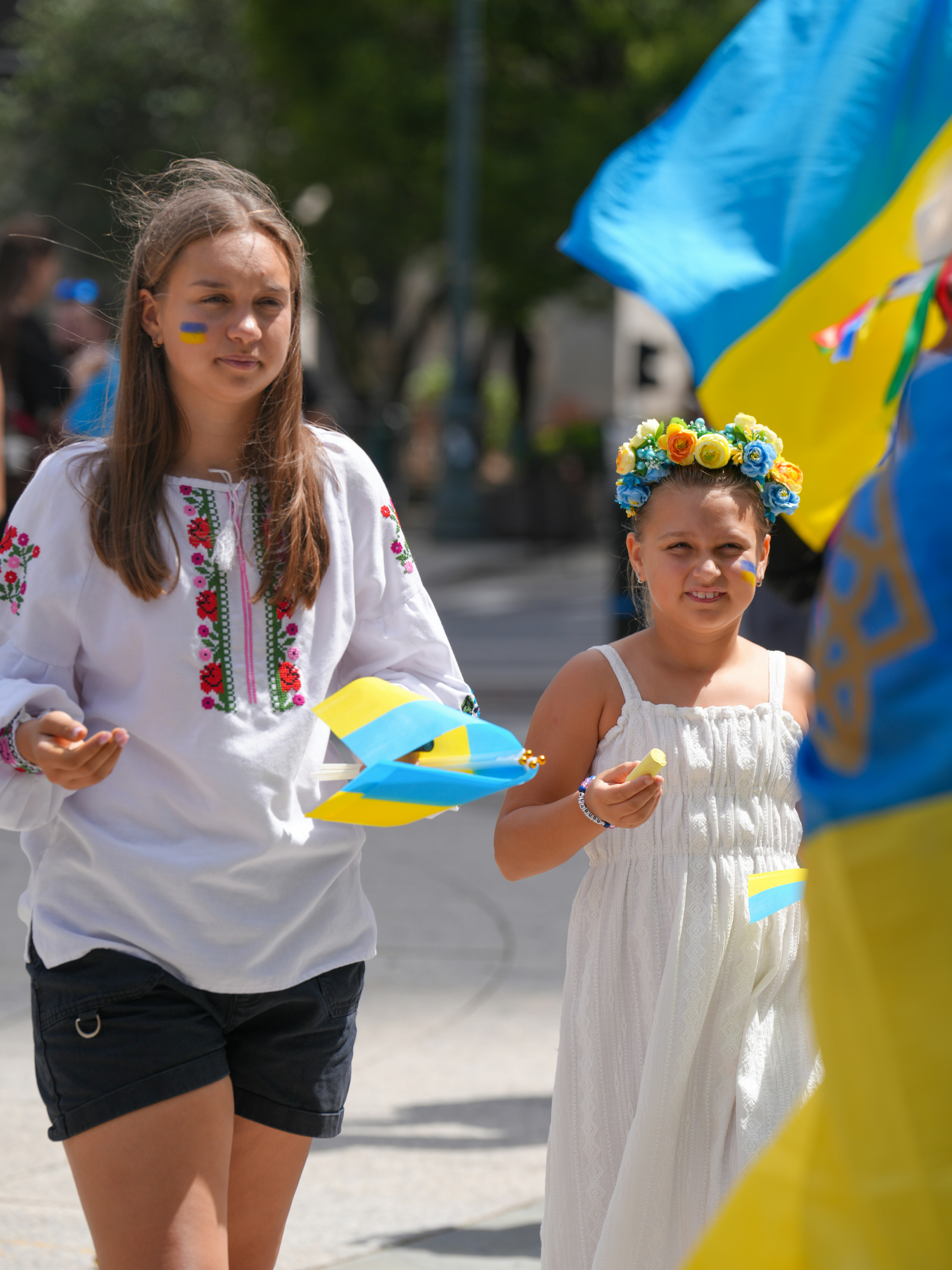 Faces in Freedom: Two Ukrainian Girls Walk Amid Flags and Sunlit Street