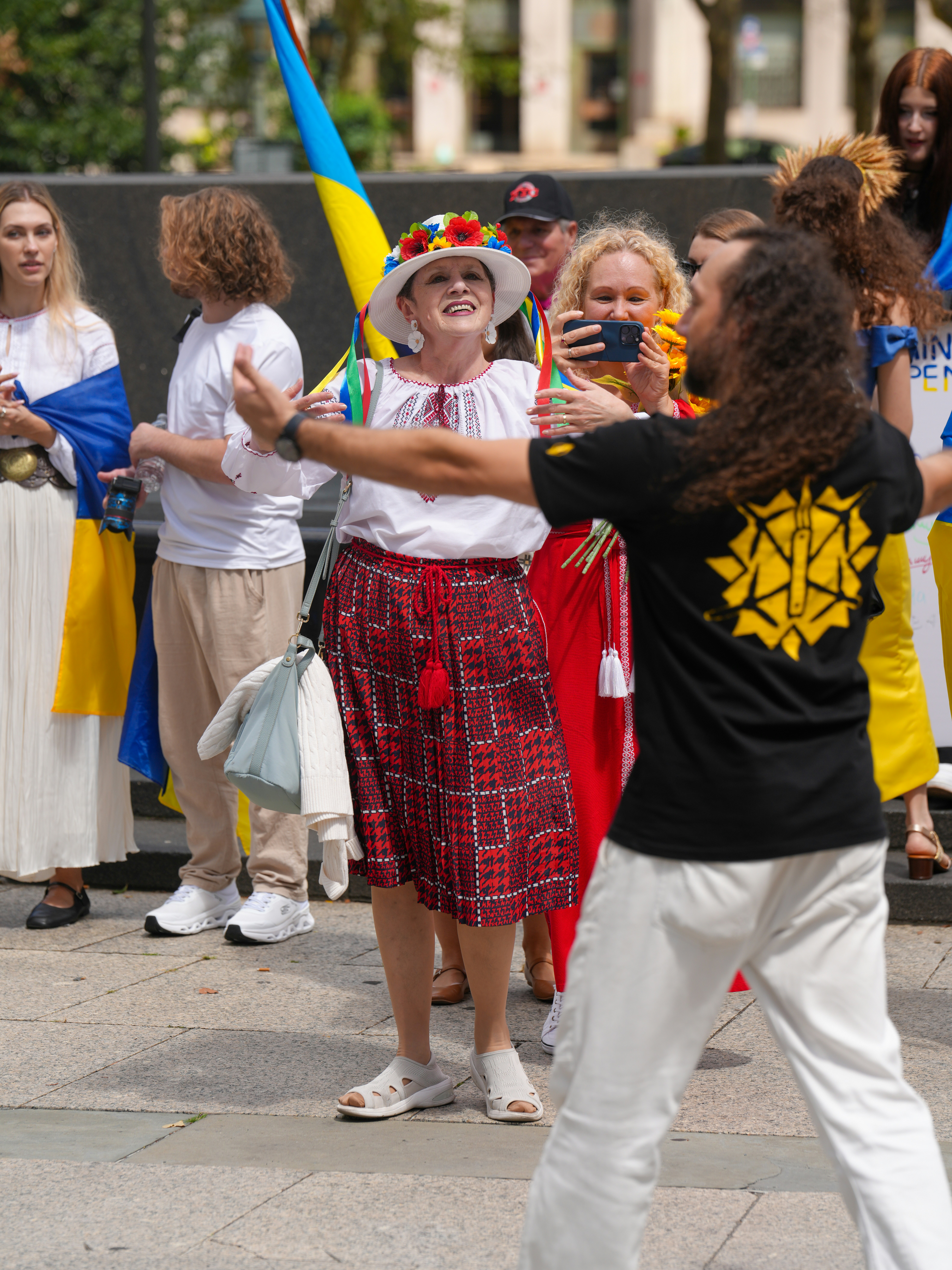 Vibrant street scene: a dancer in a white hat leads a crowd of colorful flag-bearing onlookers