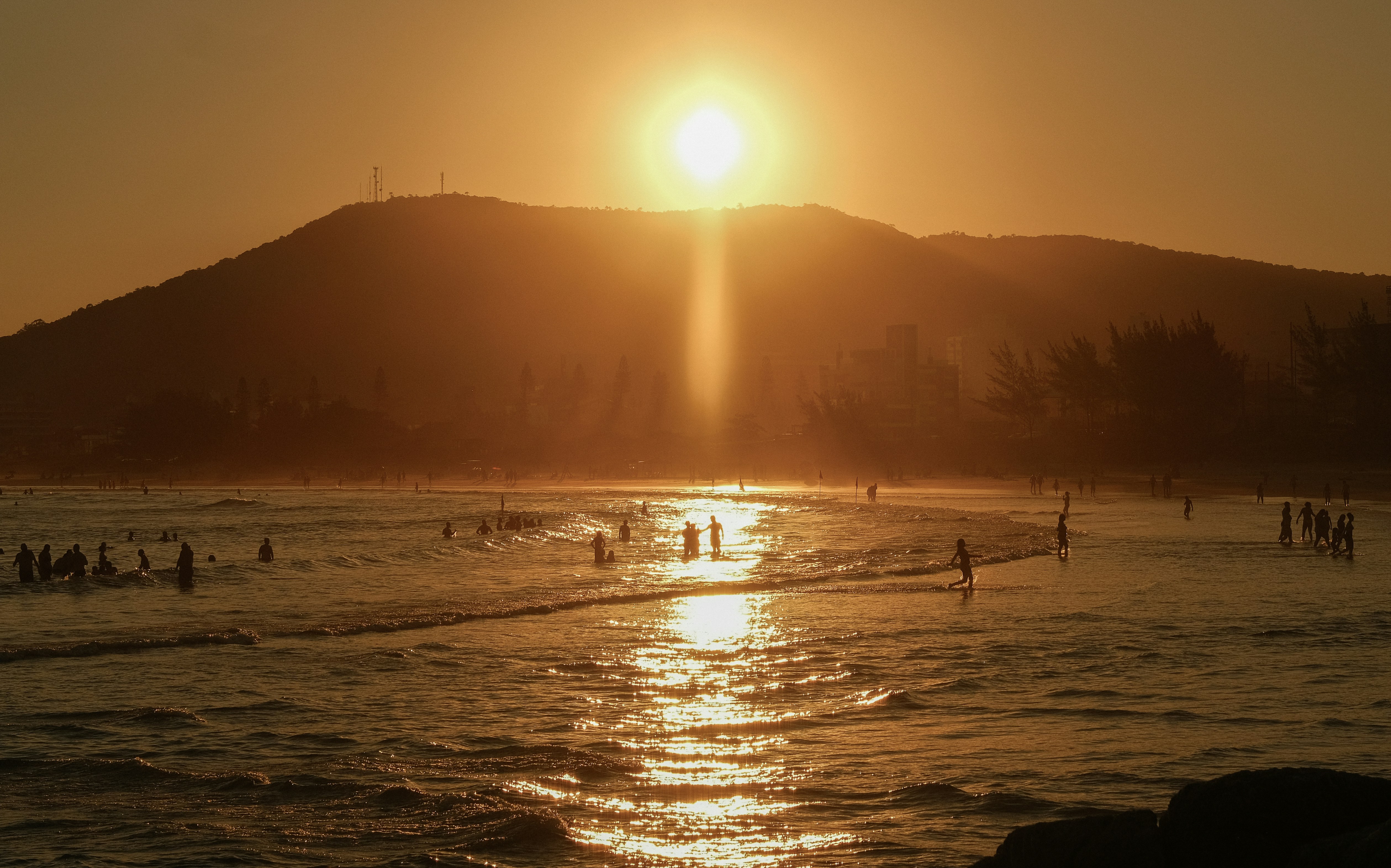 Sunlit shoreline: swimmers and sparkling tide beneath a golden sunset