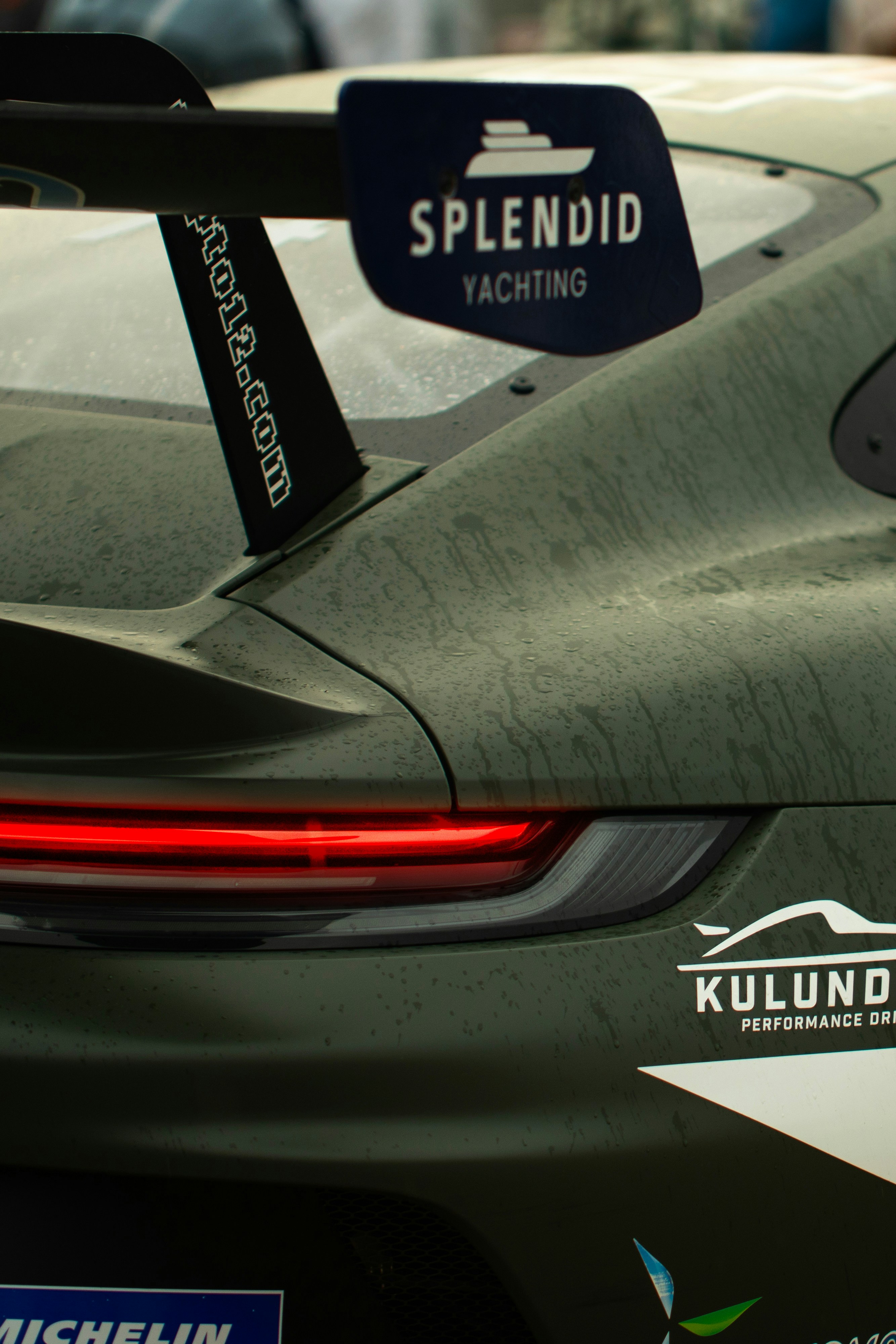 Glossy car rear with sponsor decals and a red taillight accent; a winglet and logos indicate a racing setup. Note: this is a car graphics/decals shot.