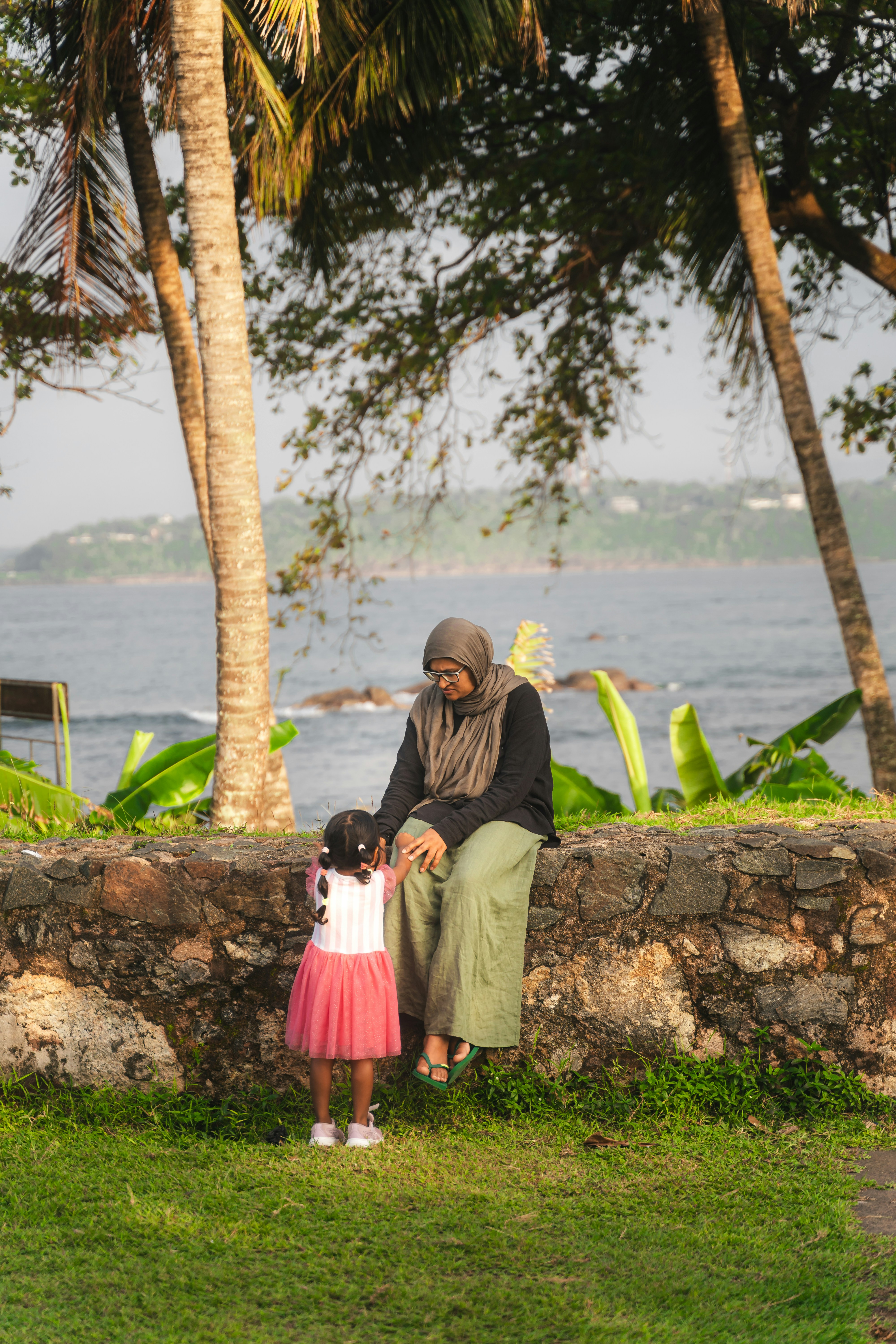 Mother and granddaughter by the sea wall under swaying palms