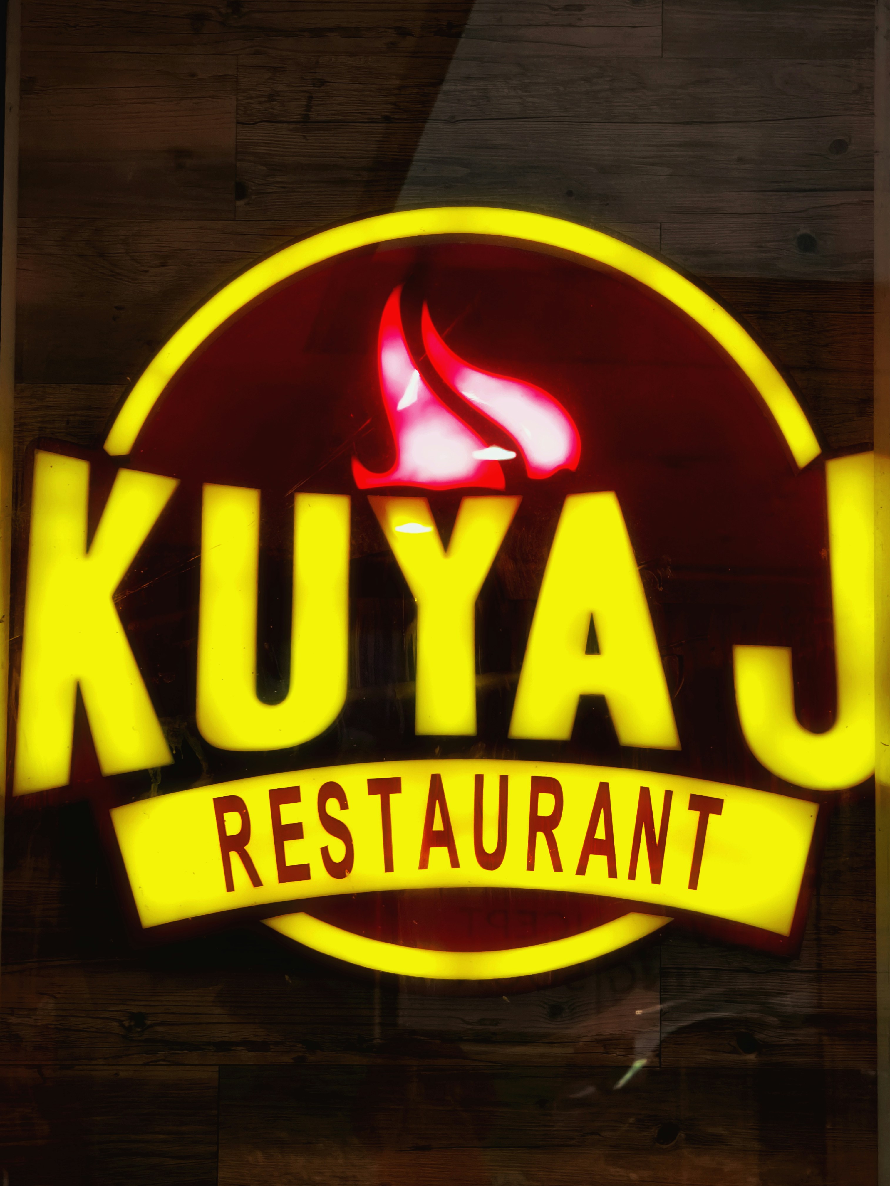 Neon Flame: KUYA J Sign Ablaze in Dim Wood Backdrop