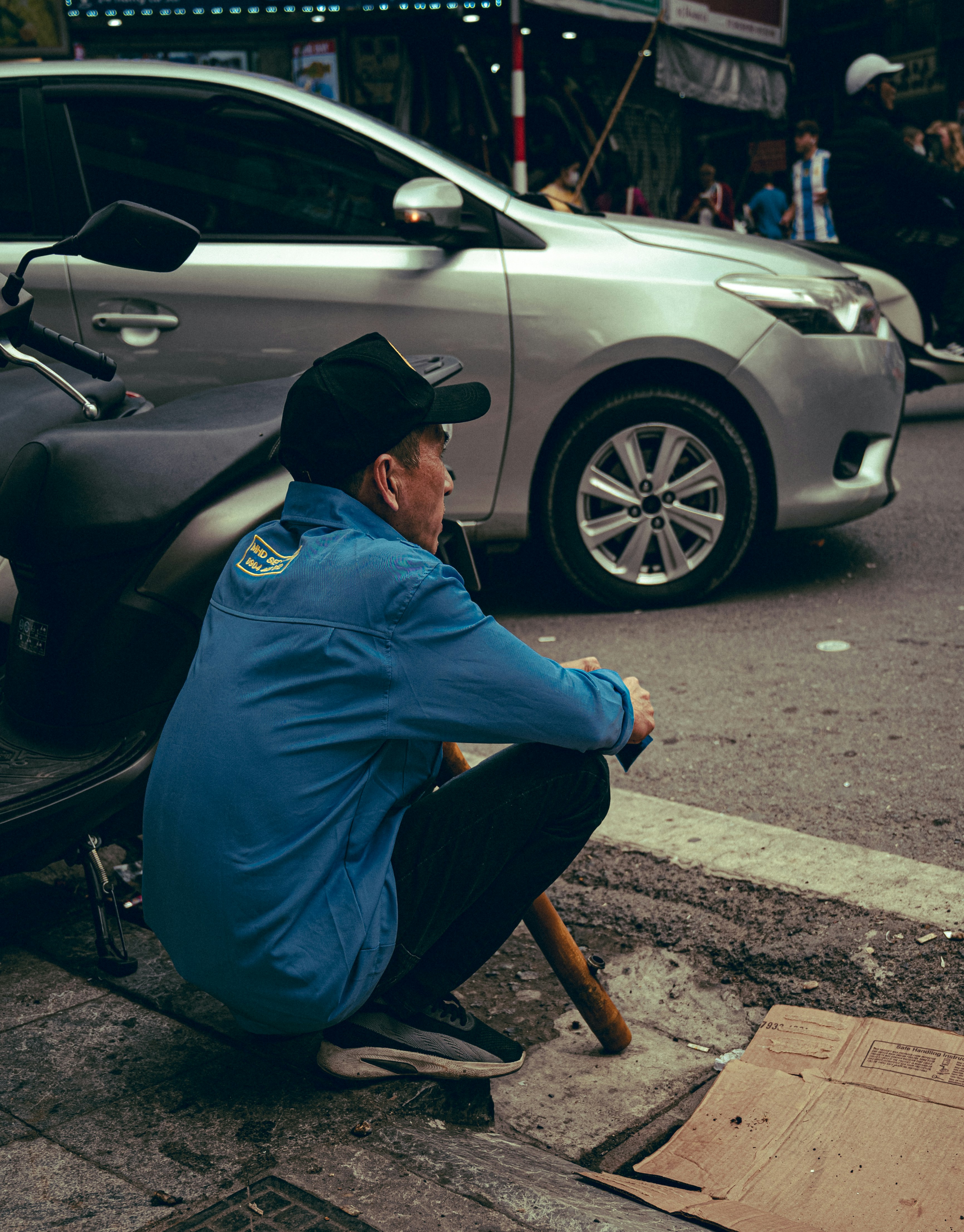 Street Respite: A Blue-Jacketed Worker Pauses beside a Parked Car