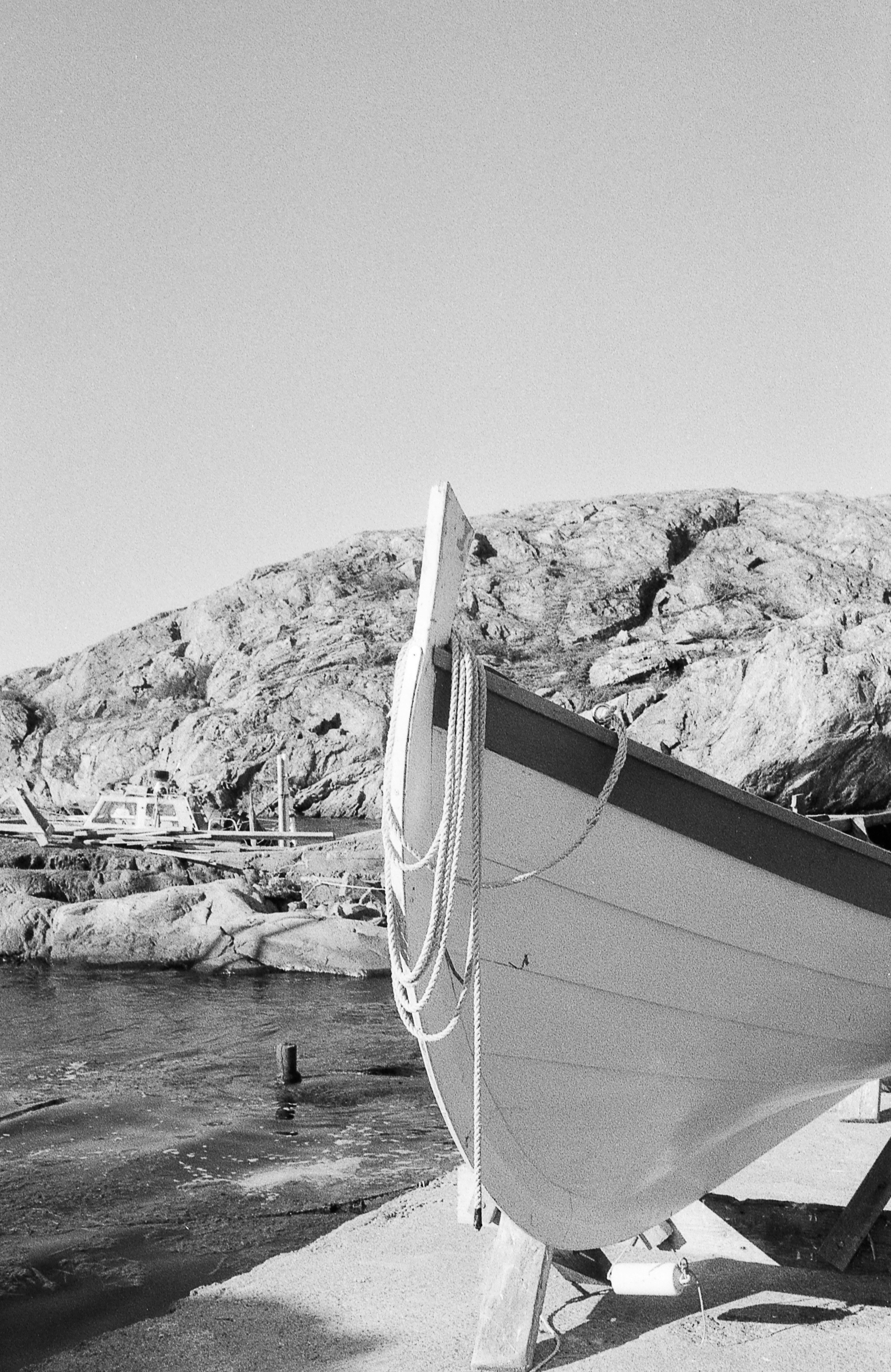 A boat rests on the shore with rocky hills behind.