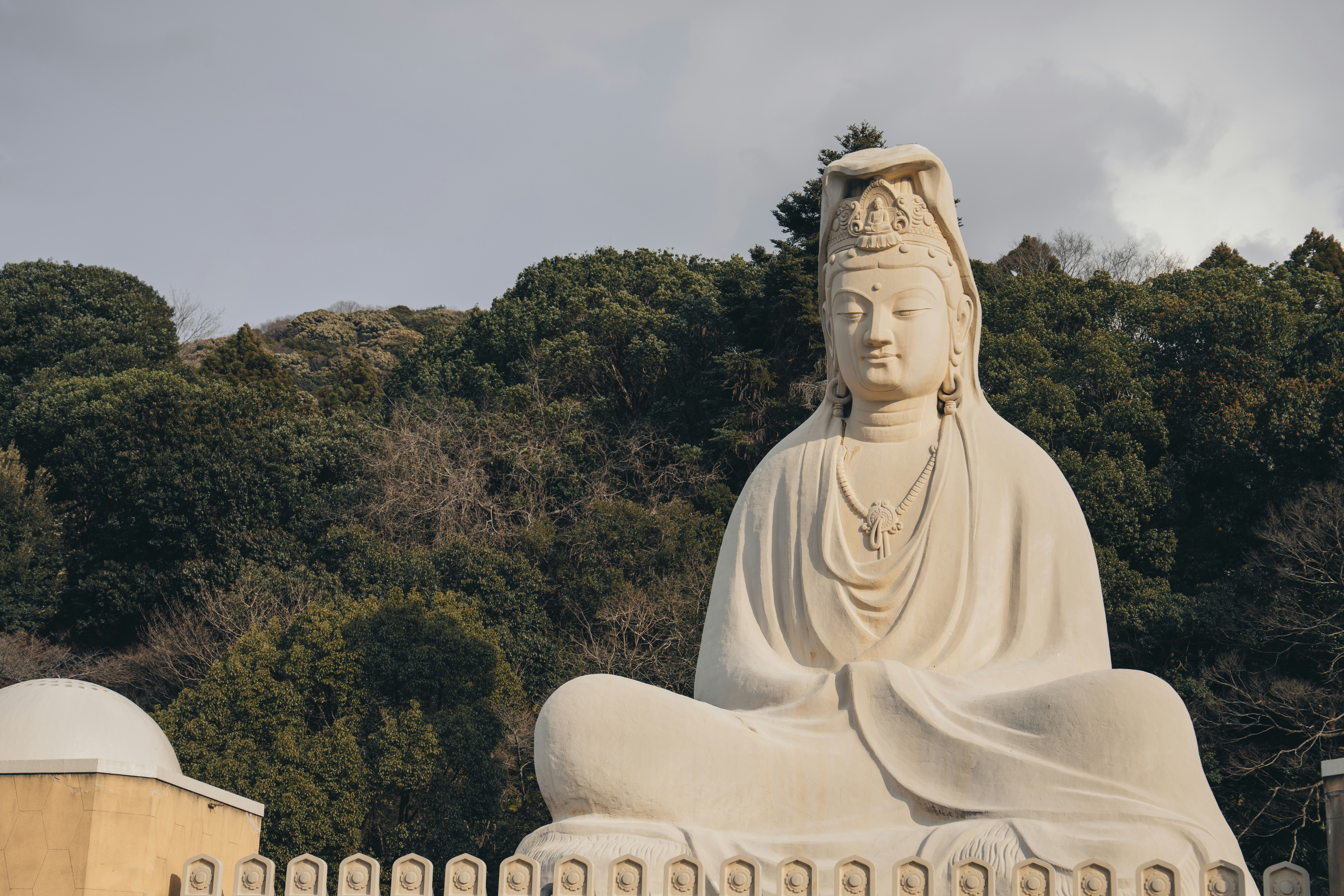 Quiet Greatness: A Meditative Statue Surrounded by Silent Pines