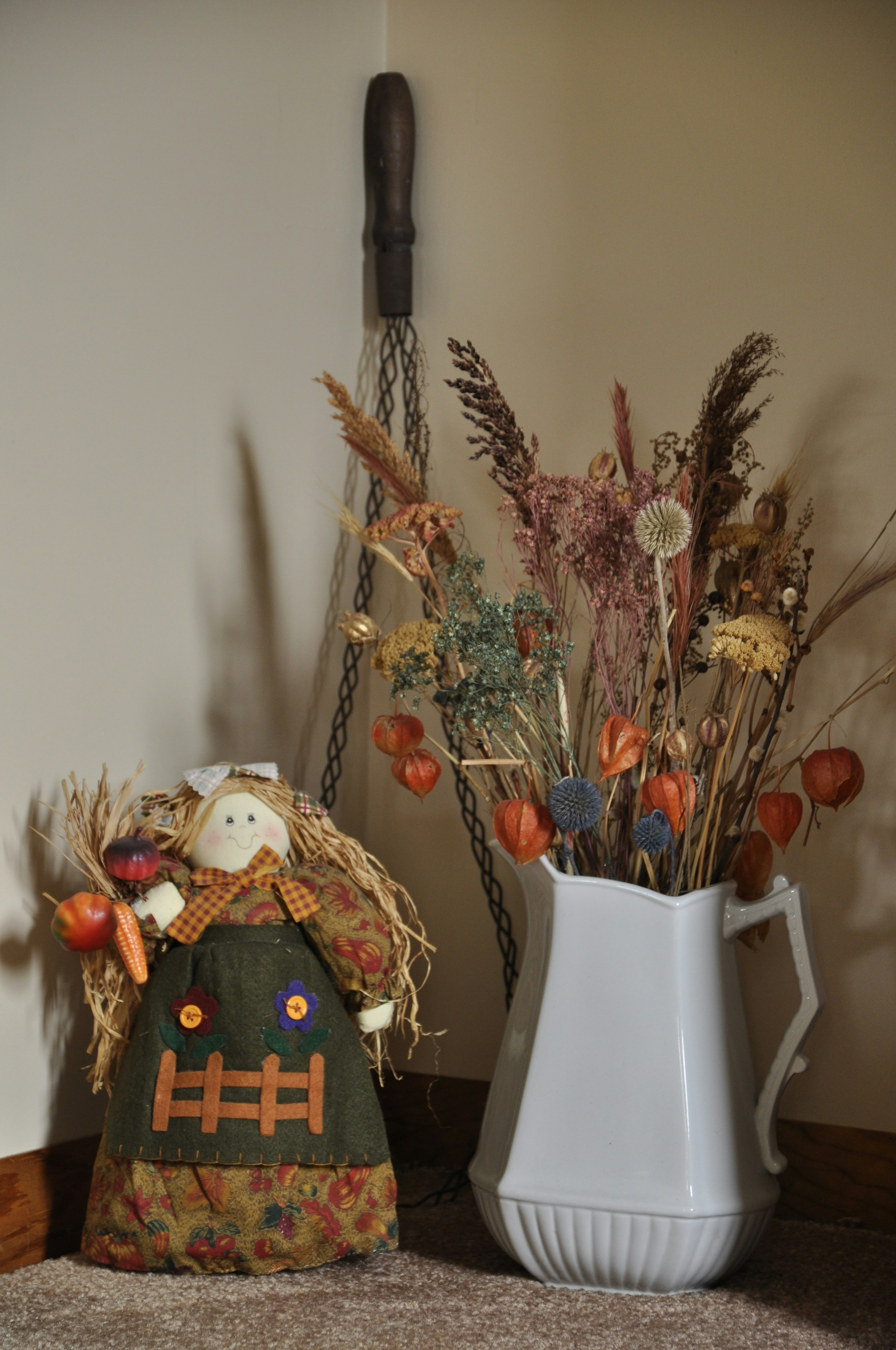 Dried bouquet in a pale pitcher next to a rustic cloth doll on a shelf