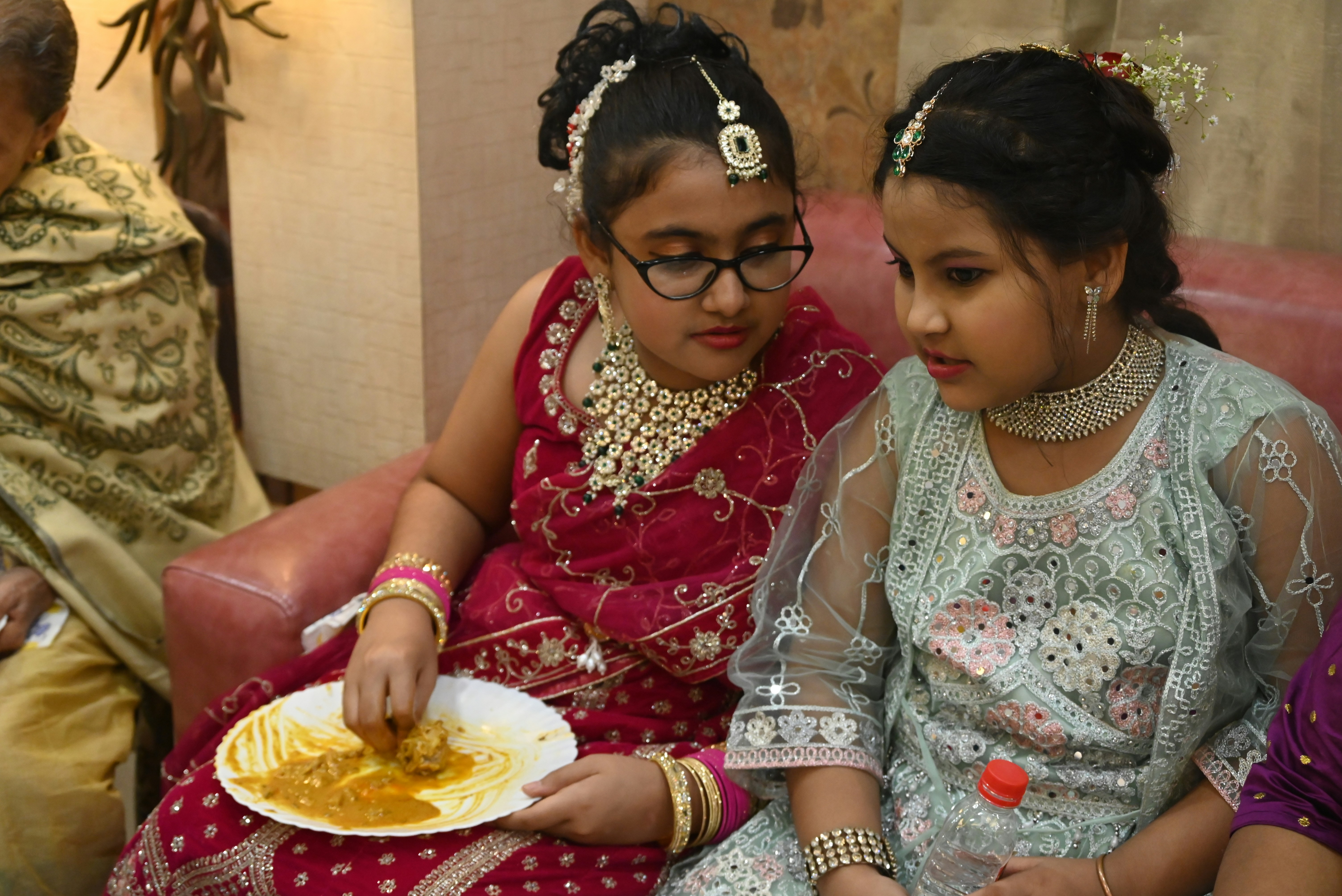 Two richly dressed girls sharing a plate of snacks in a cozy gathering
