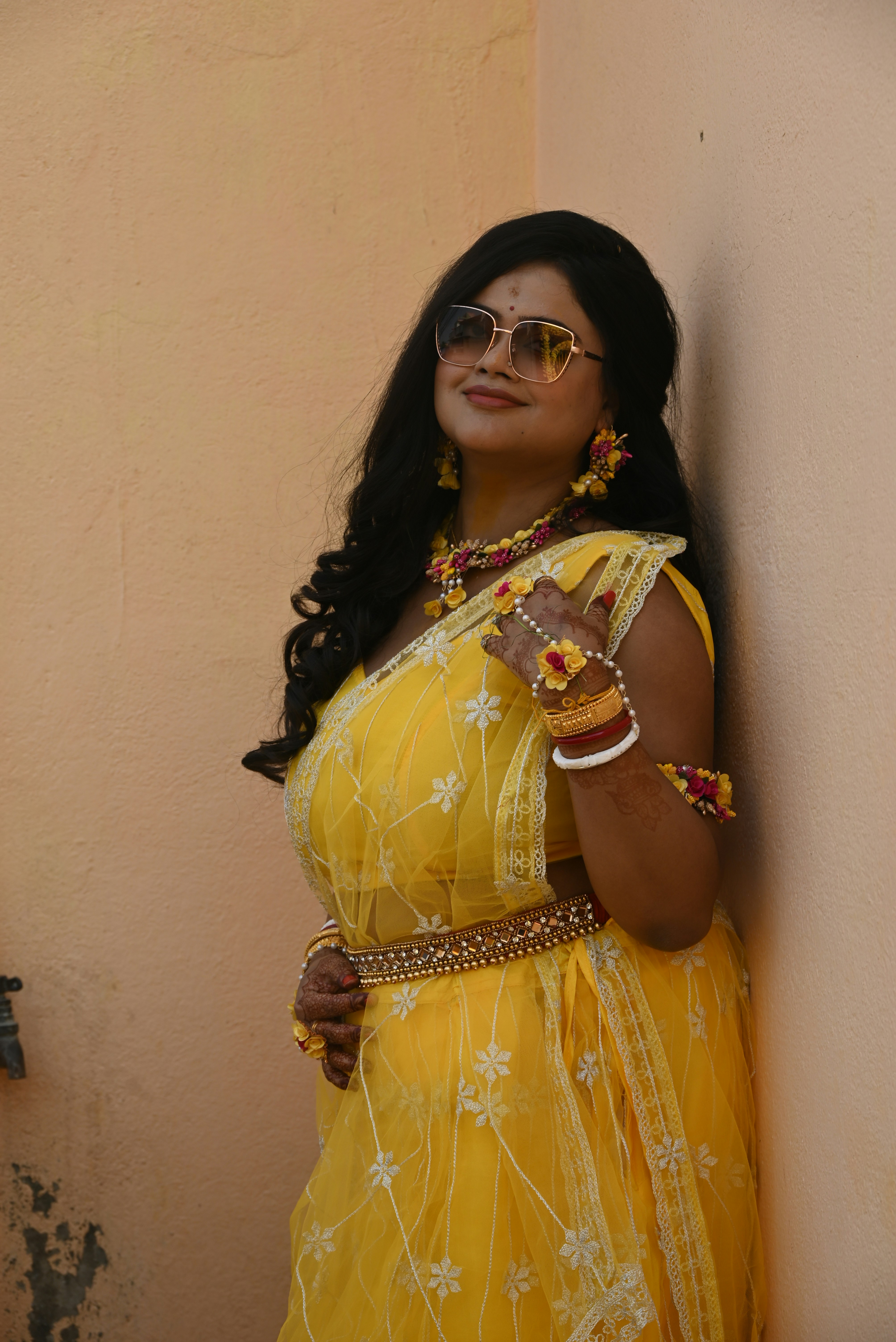 A woman in a yellow sari with sunglasses and jewelry.