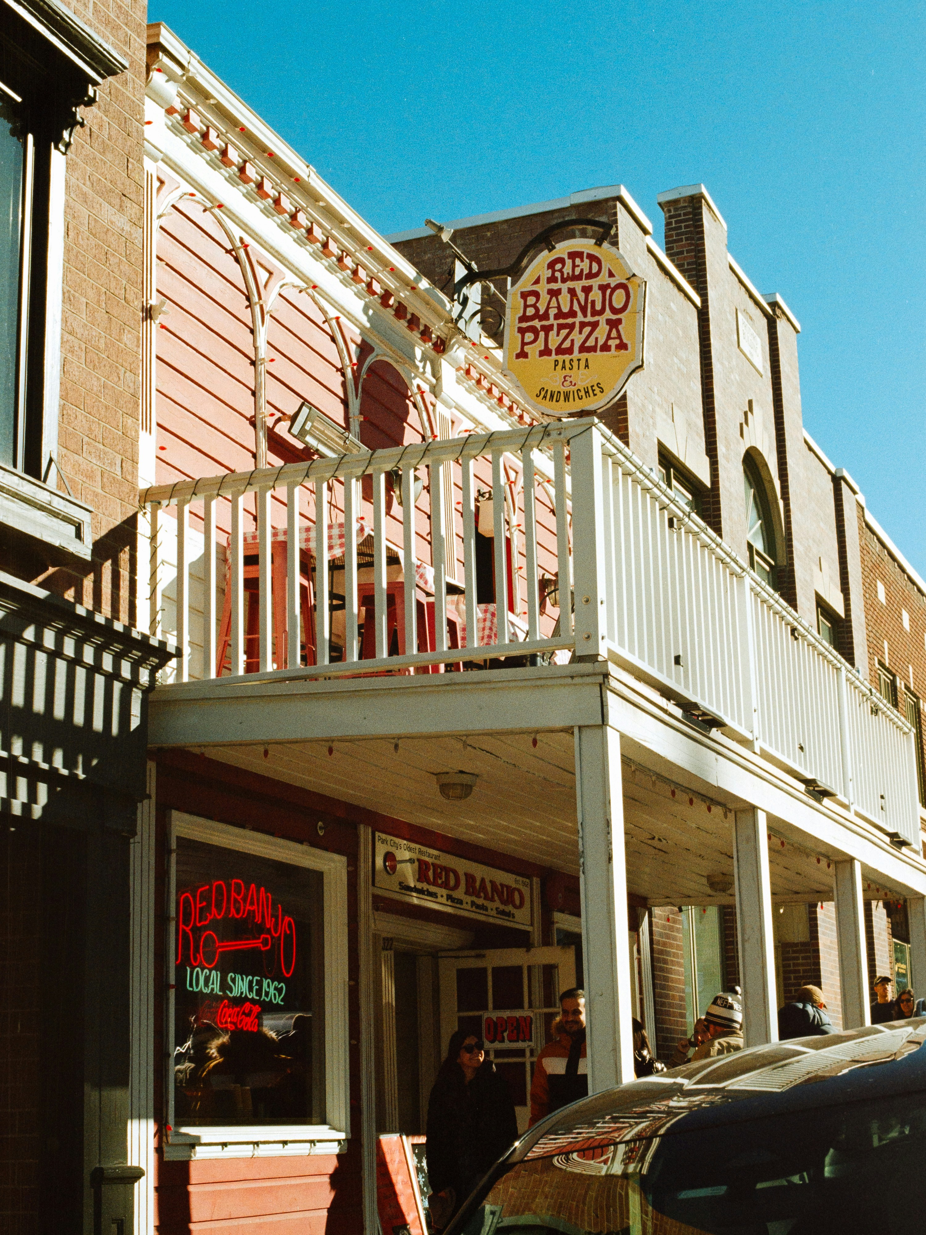 Red Banjo Pizza: Vintage storefront under a sunlit balcony