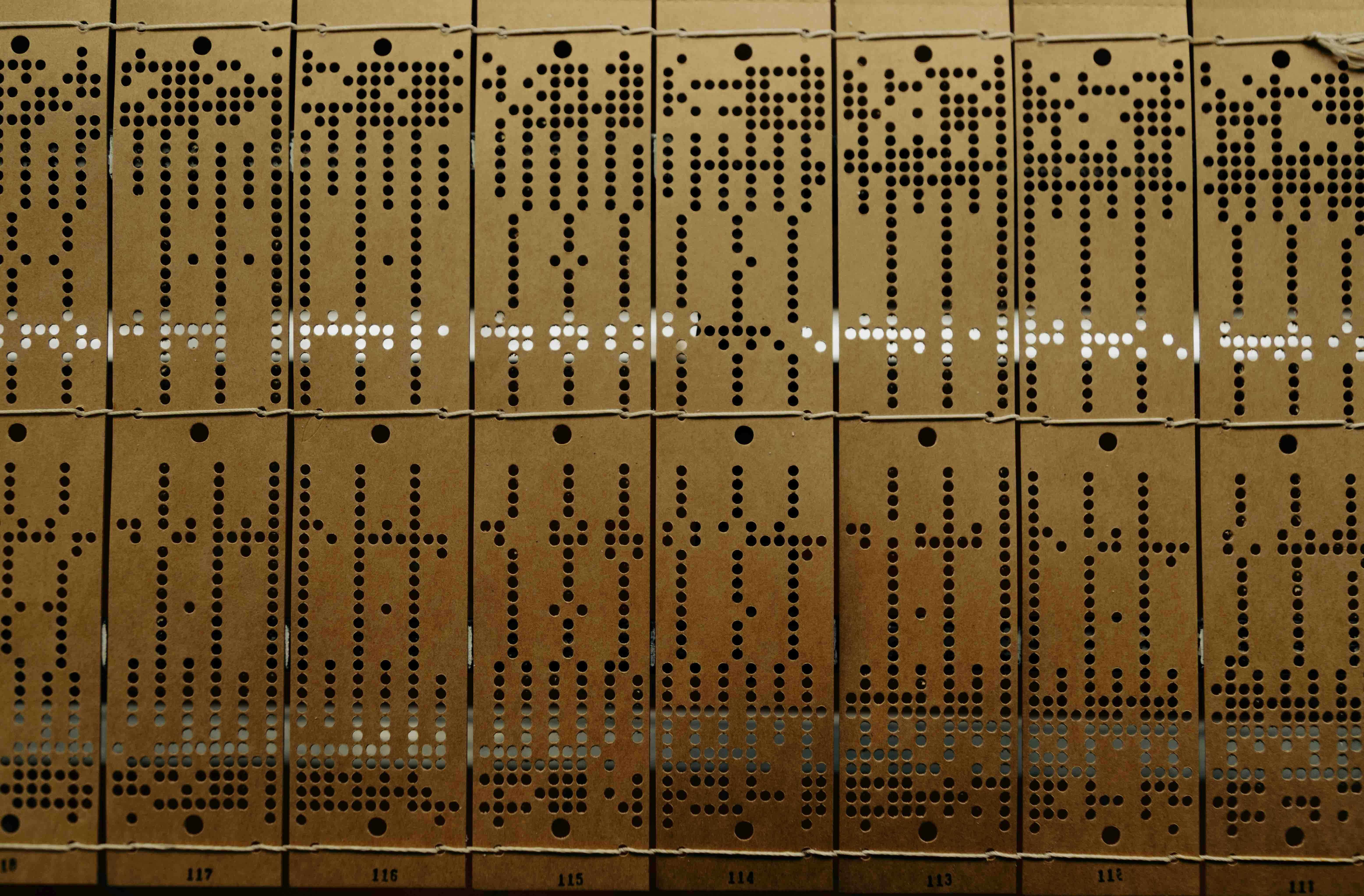 Close-up of a brown metal surface with a dense grid of punched holes and a white dashed line across the center, resembling a perforated plate or label strip.